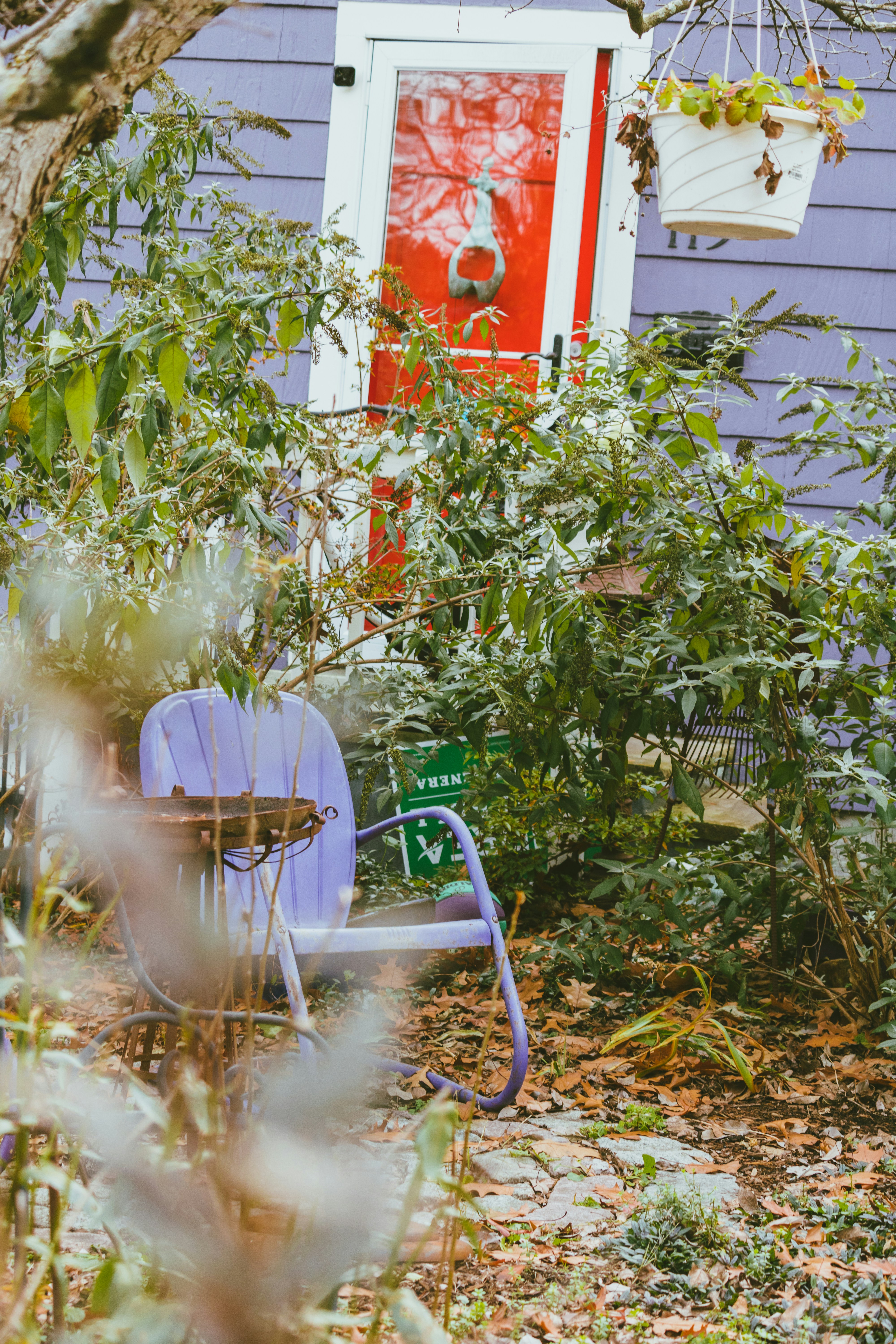 Crimson Doorway in a Purple Wall, Framed by Verdant Foliage and a Lavender Chair