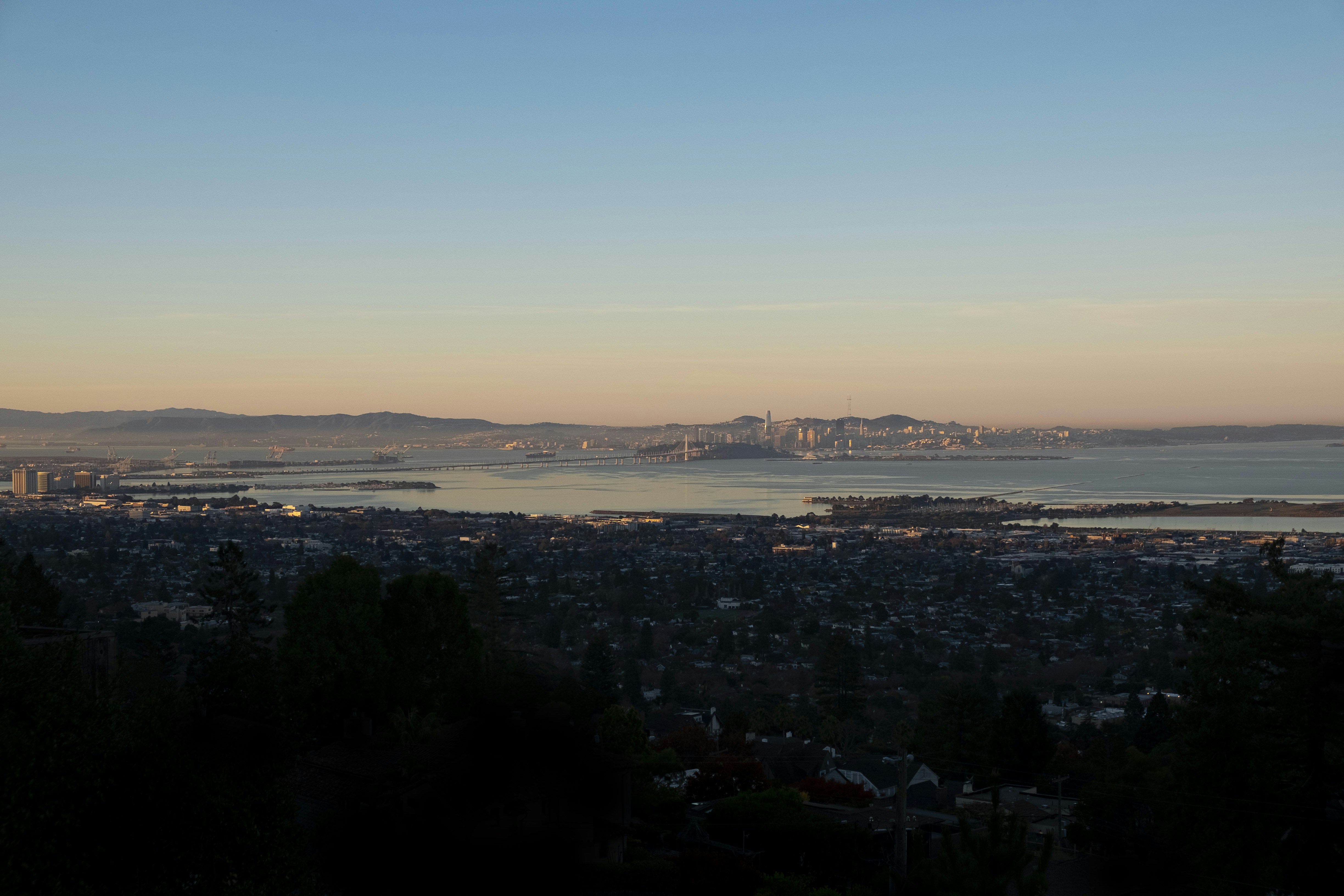 View of San Francisco Bay at dawn with cityscape and distant hills under a clear sky.