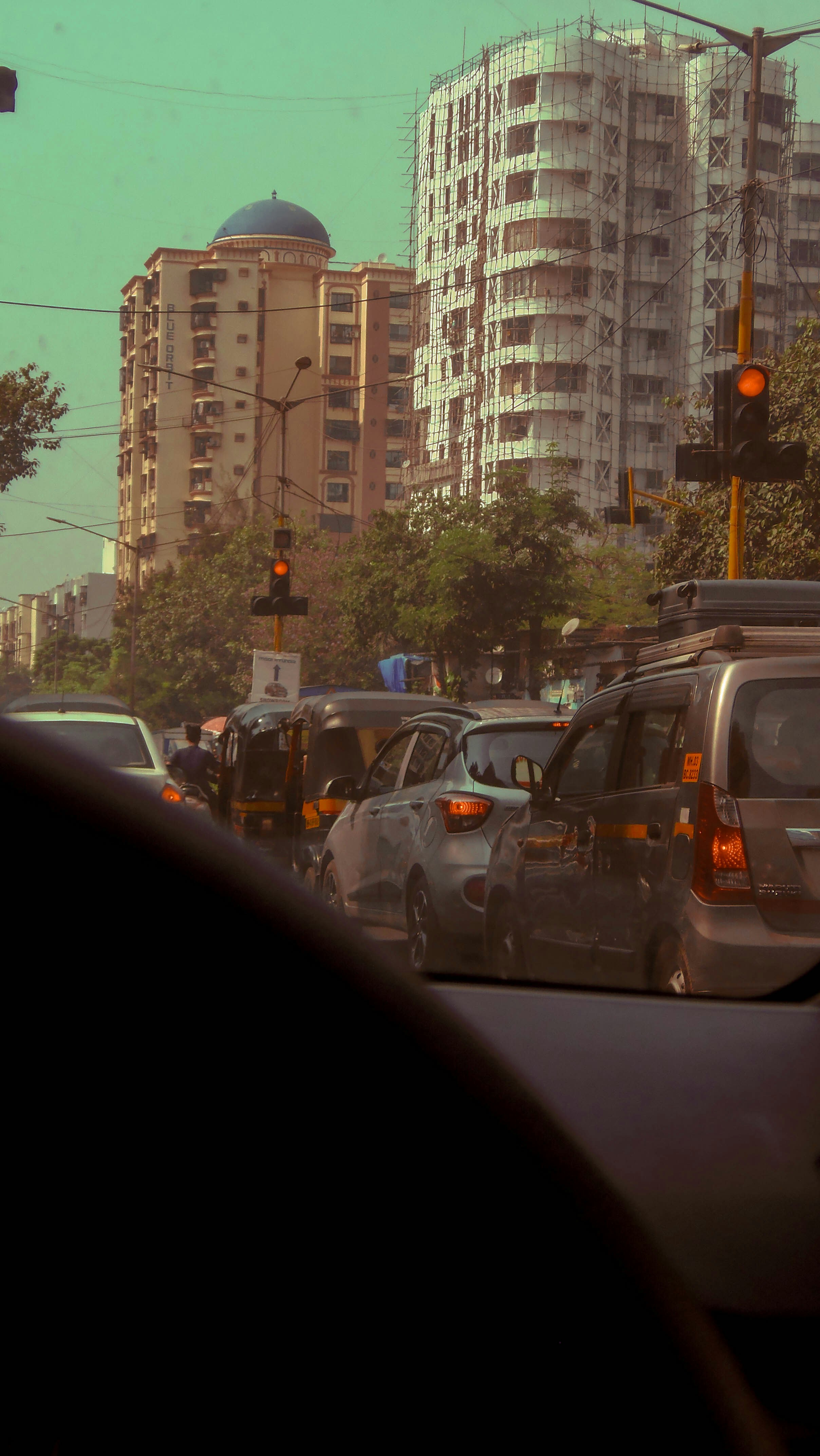 Urban street scene featuring a blue-domed tower beside a scaffolded high-rise, framed by dense traffic and viewed through a car window.