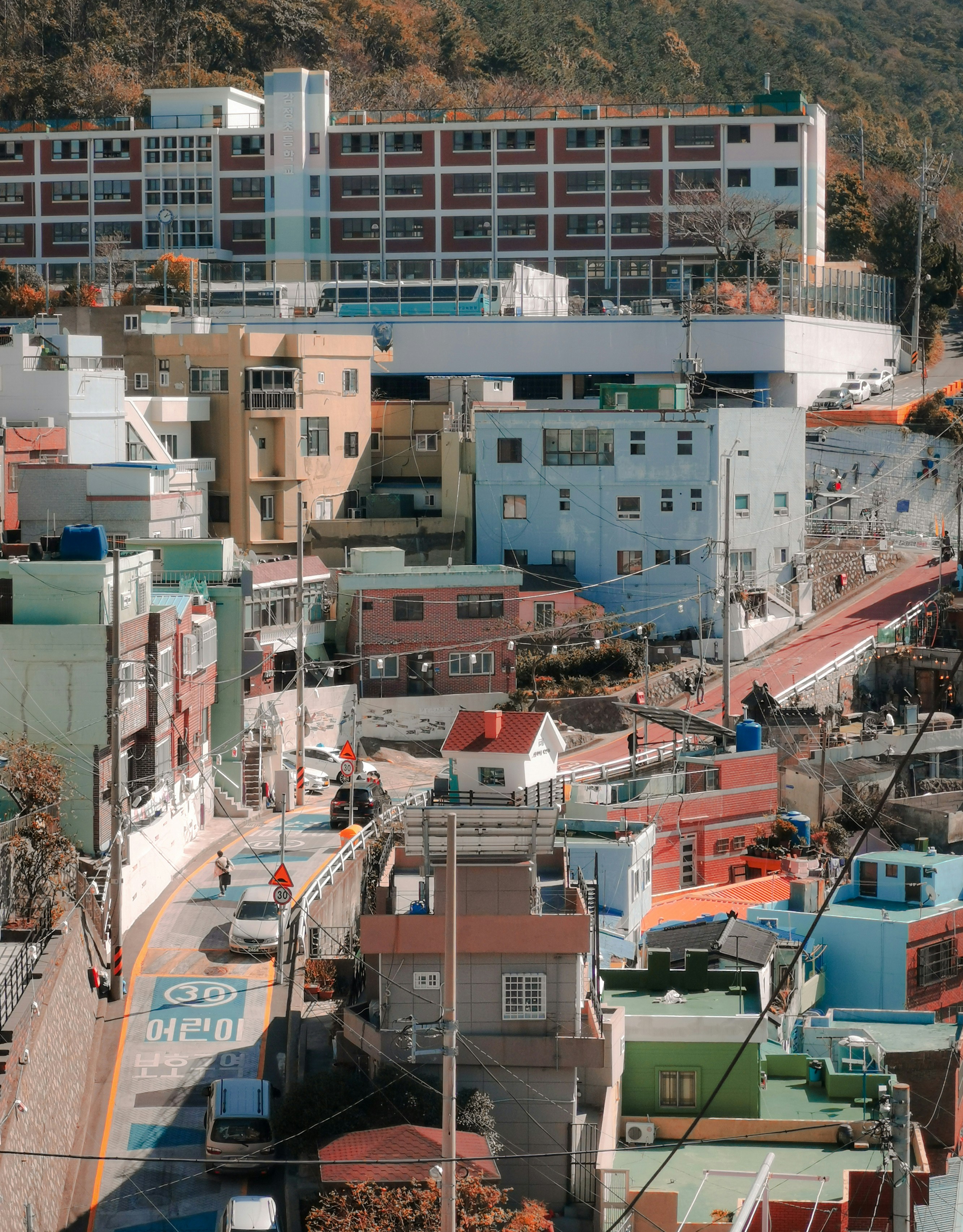Pastel houses line a curving hillside street, photographed from above in daylight, forming a dense, colorful urban mosaic. The scene emphasizes the neighborhood's layout and palette.