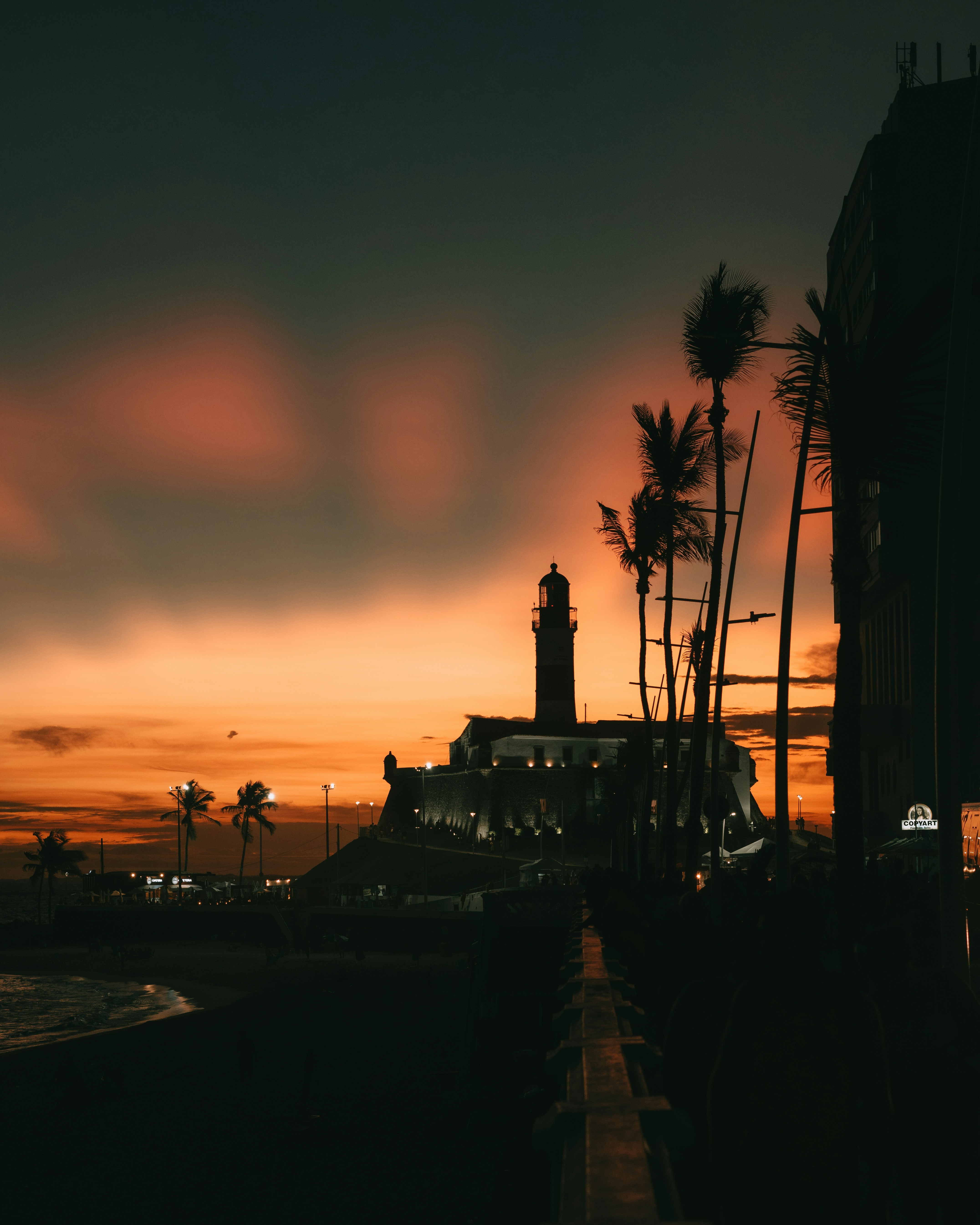 Lighthouse Silhouette at Dusk: Palm-Fringed Harbor Under a Molten Sky