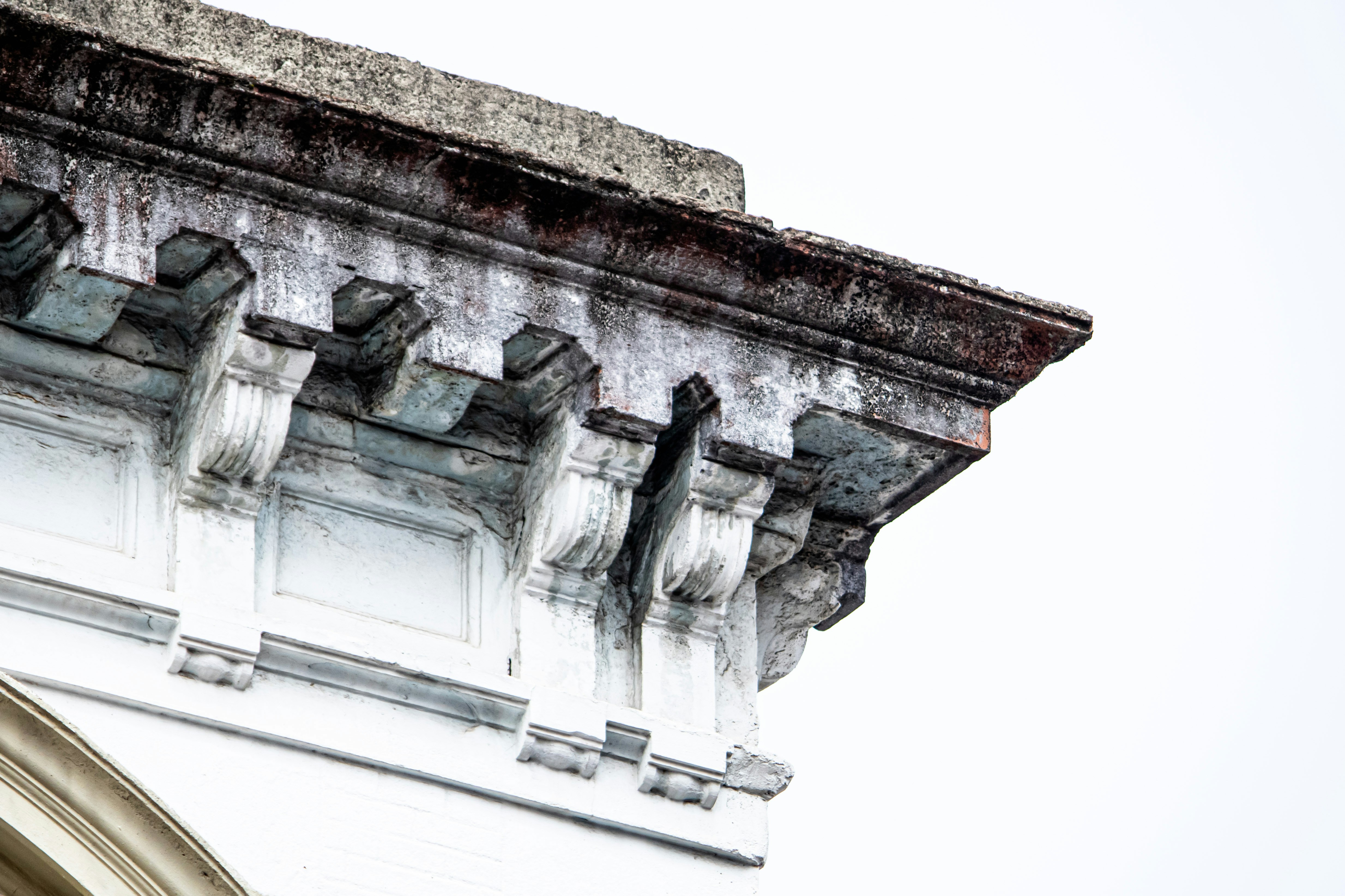 Weathered Cornice Close-Up: Ornate Brackets Against a Pale Sky