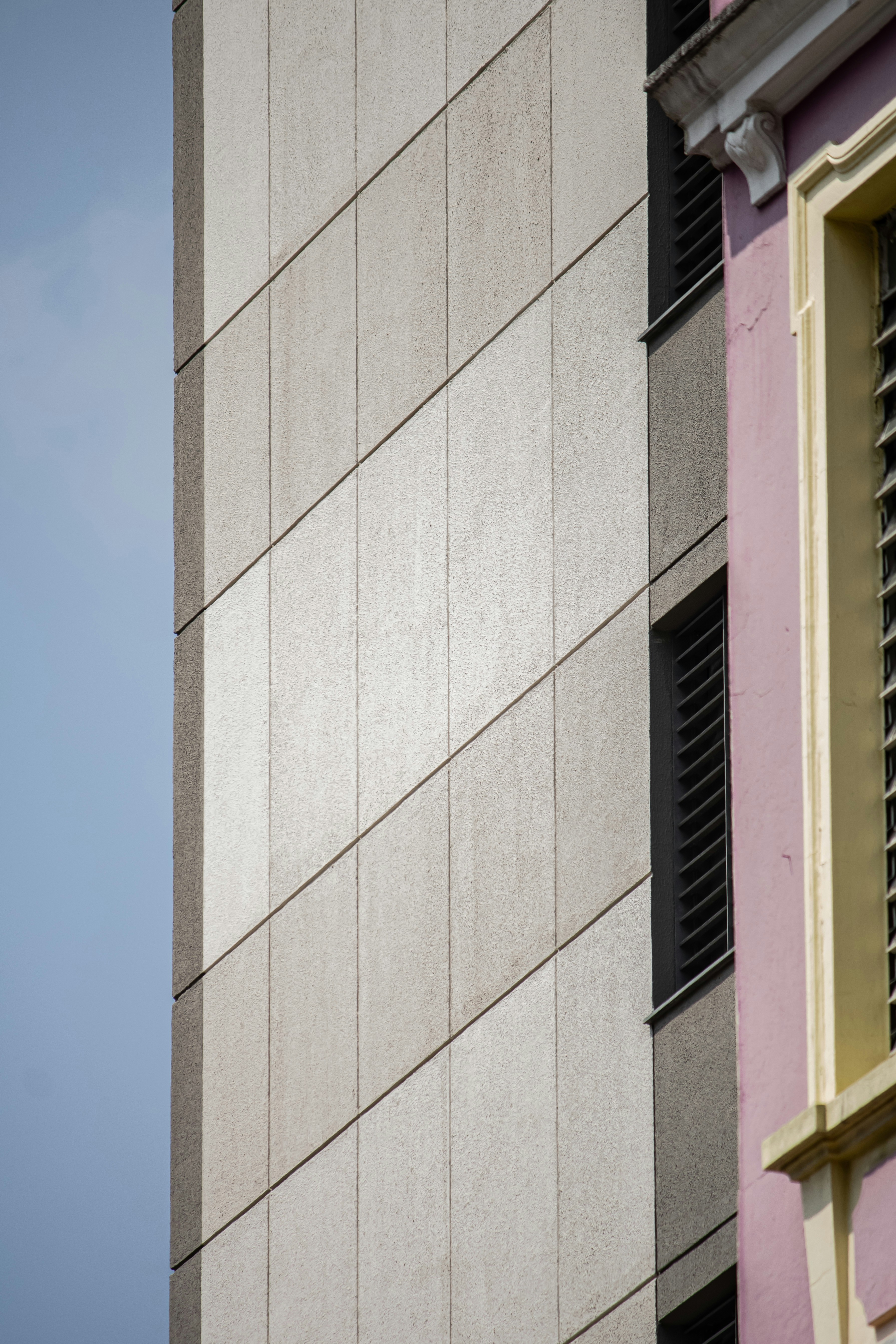 Pastel Facade Lines: Pink Window Anchors a Sunlit Concrete Wall