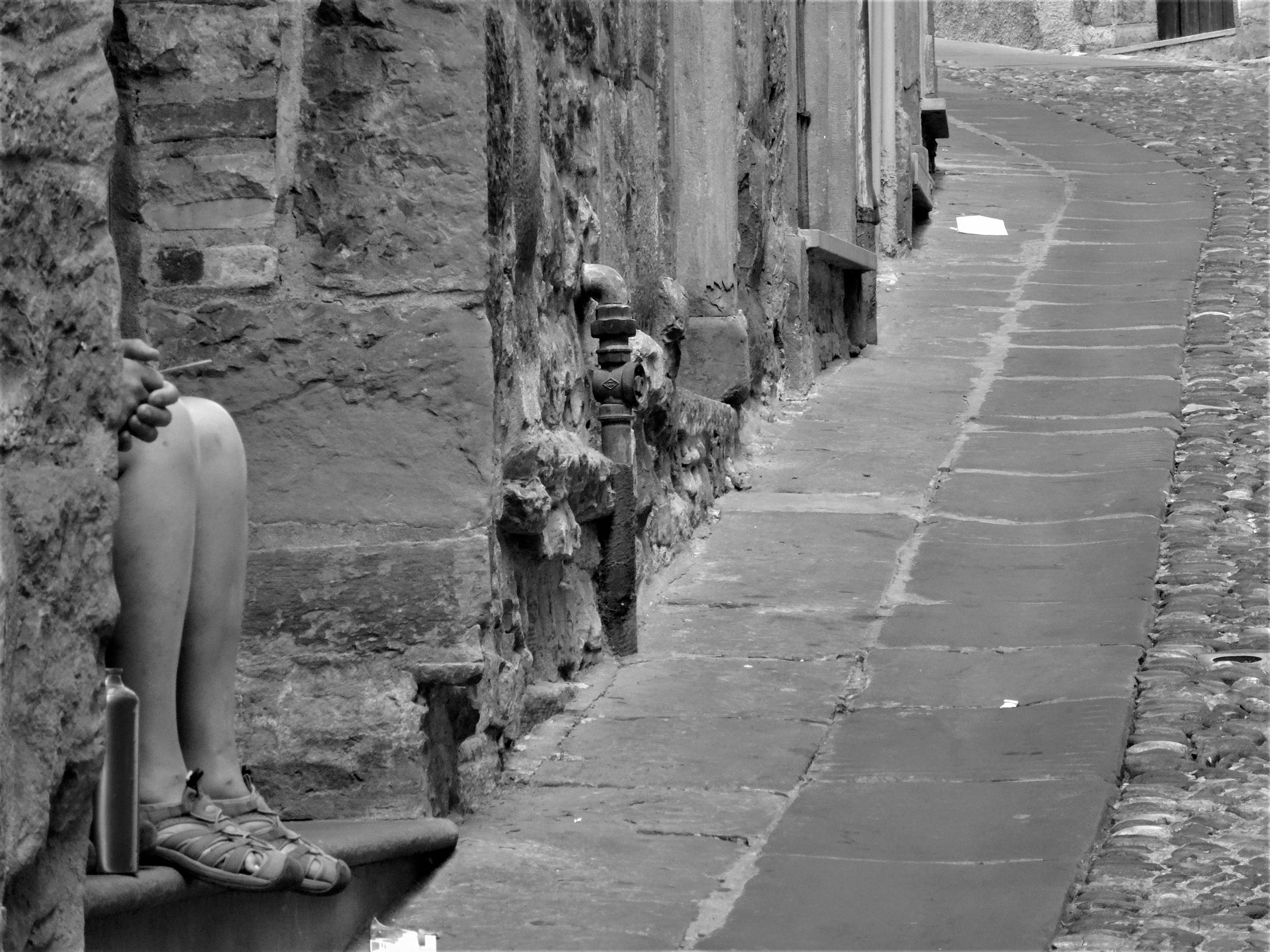 Black and white photo of a narrow cobblestone alley with sculptures embedded in the stone wall.