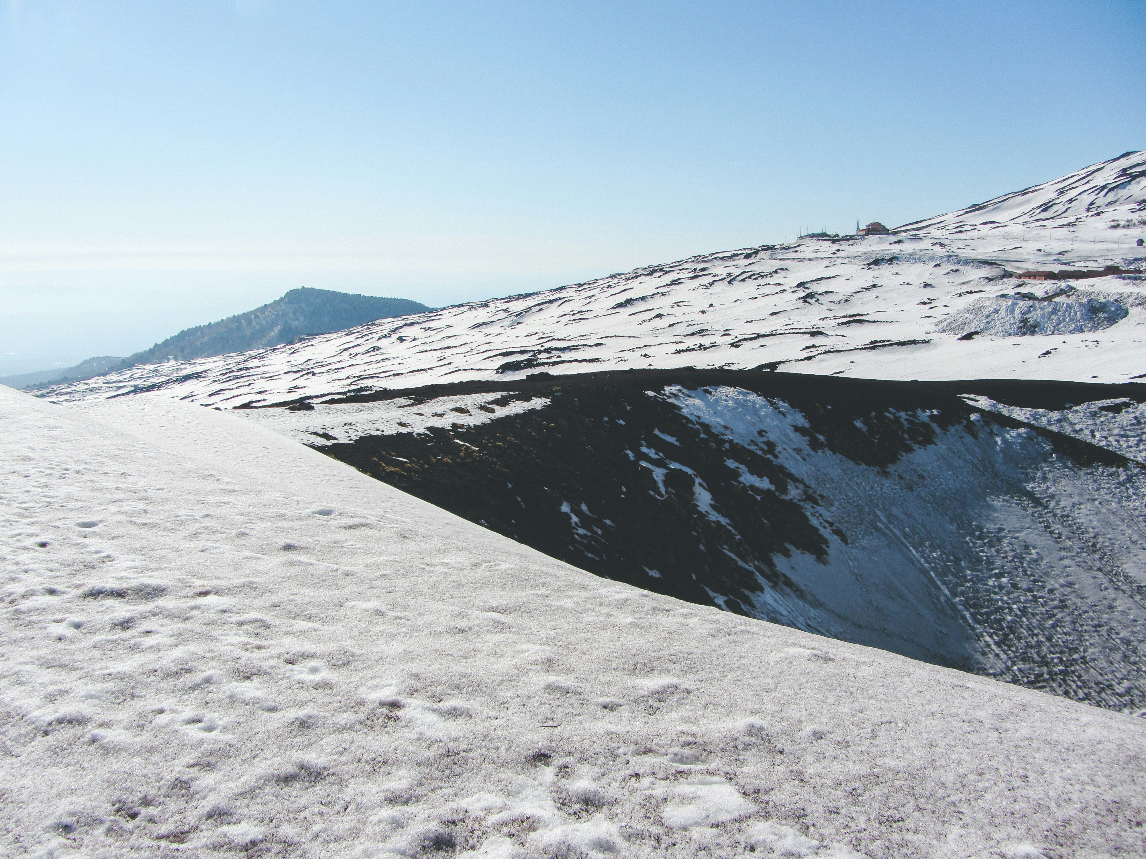 Snow-covered mountain slope with distant peaks under a clear blue sky.