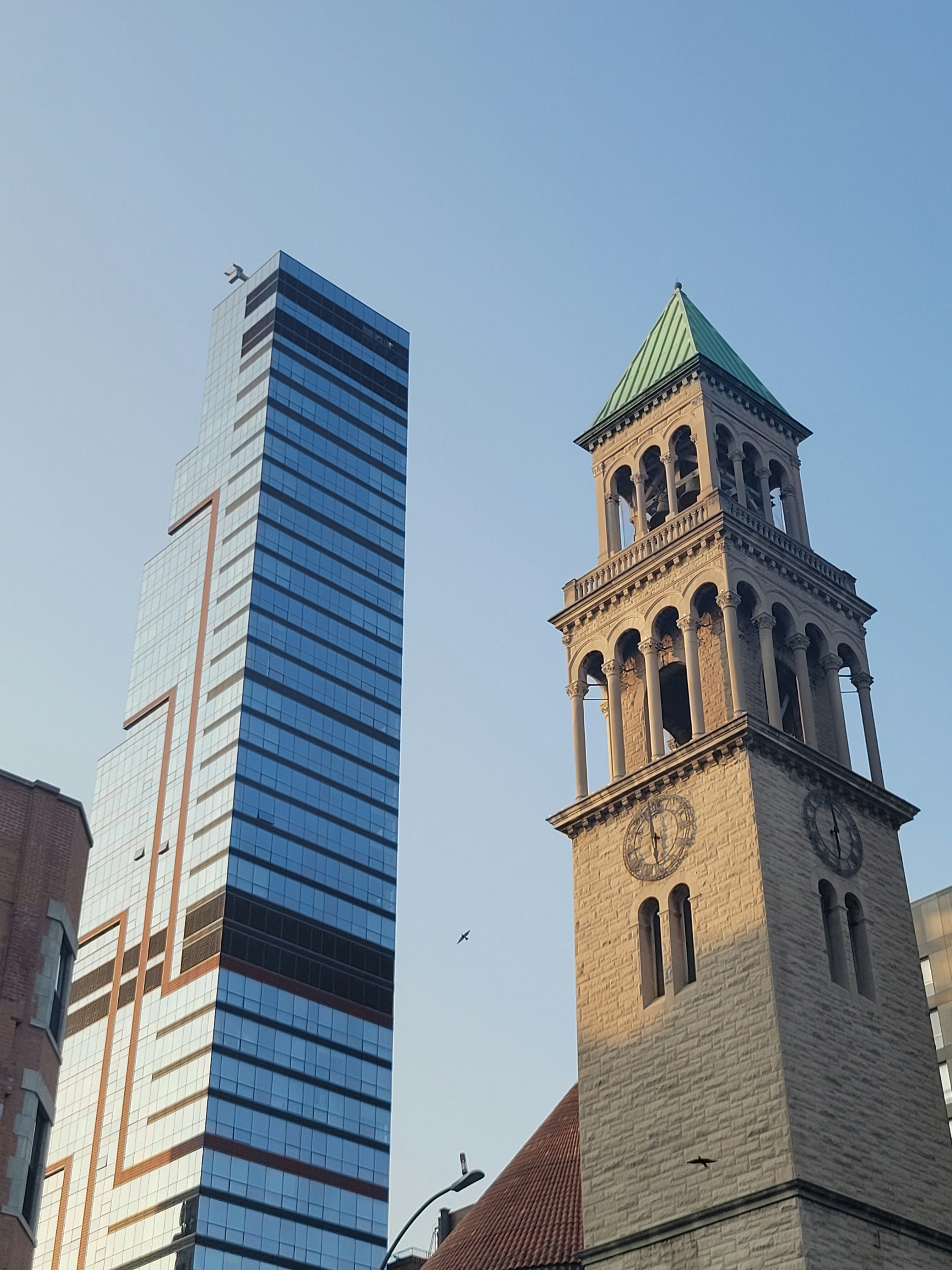Modern skyscraper juxtaposed with historic clock tower under a clear sky.