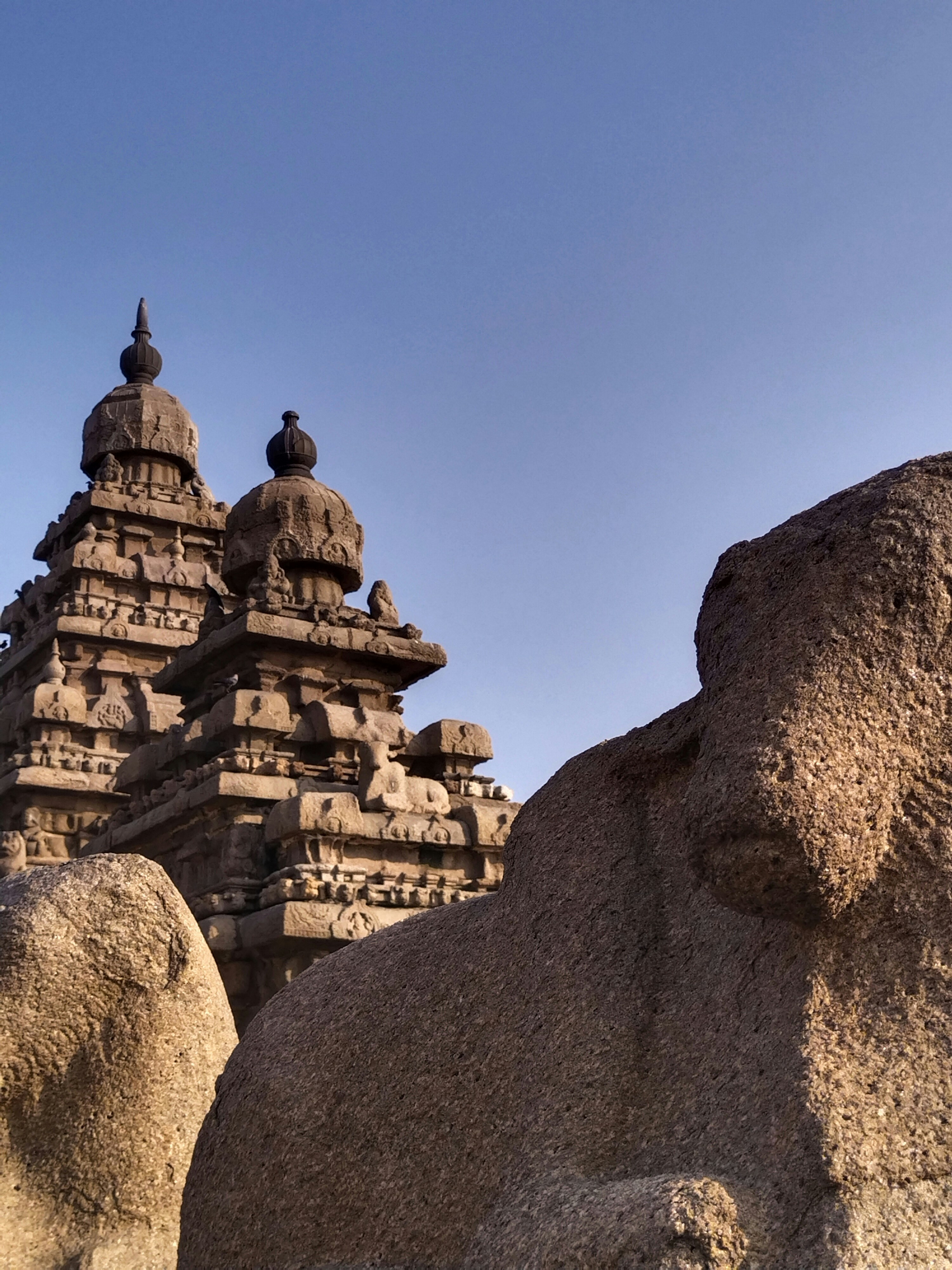 Intricate stone carvings of a temple juxtaposed with a massive granite sculpture, showcasing the artistry of historical architecture against a clear sky.