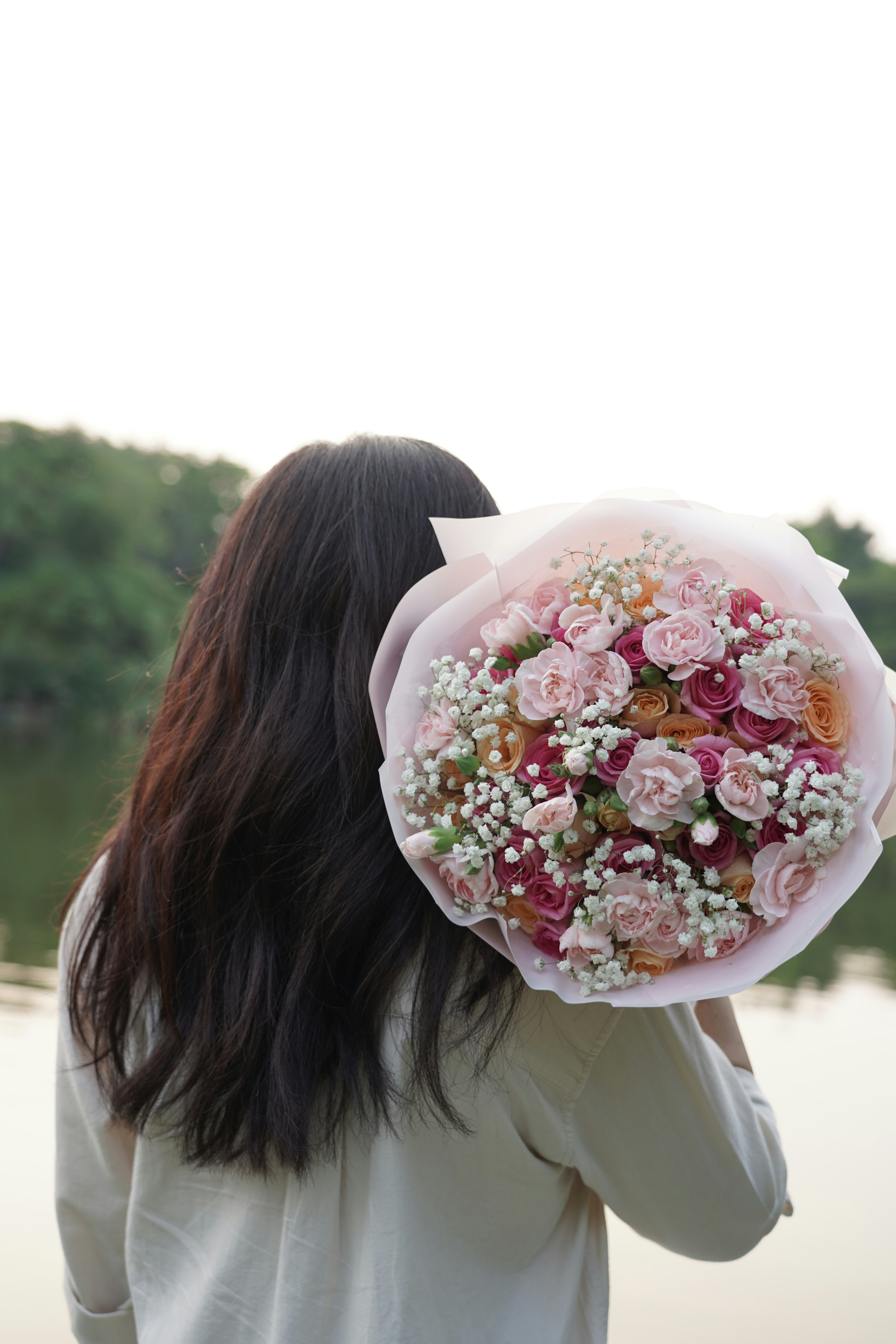Bouquet of blush roses cradled by a woman facing a serene lakeside
