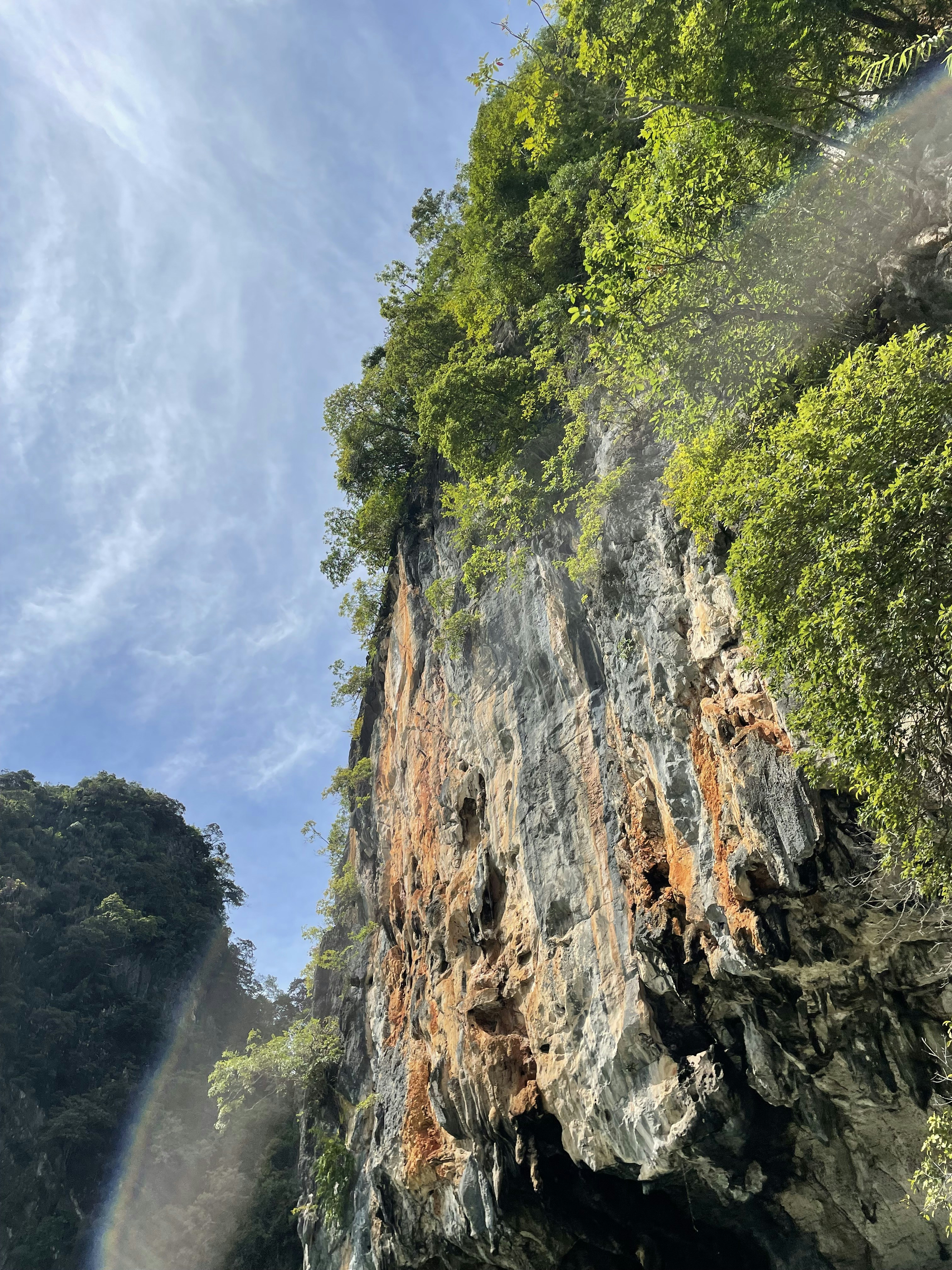 Verdant Cliff Under Azure Sky with Mist and a Subtle Rainbow