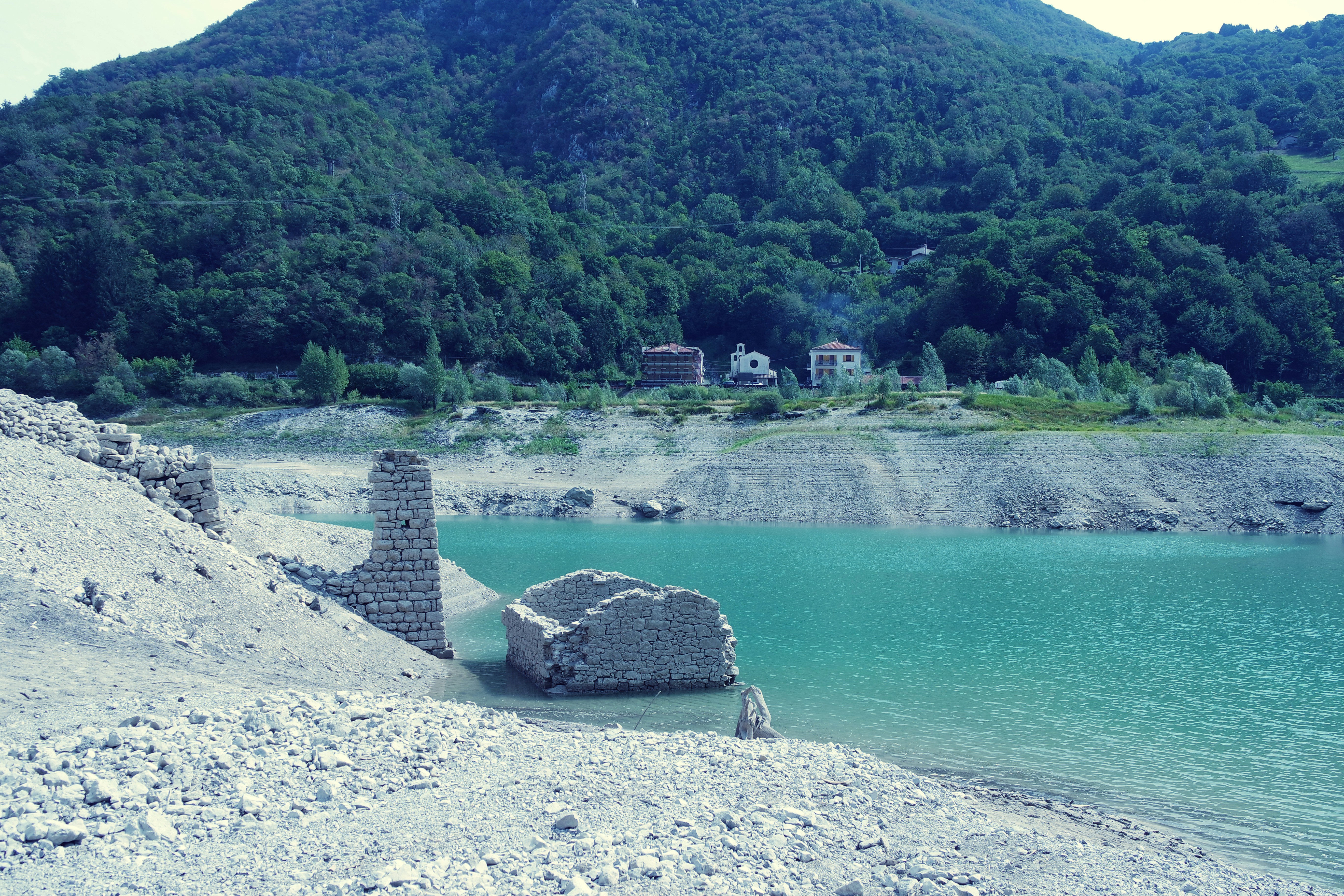 Foto Una playa rocosa con una casa y árboles al fondo – Imagen Lago de ...