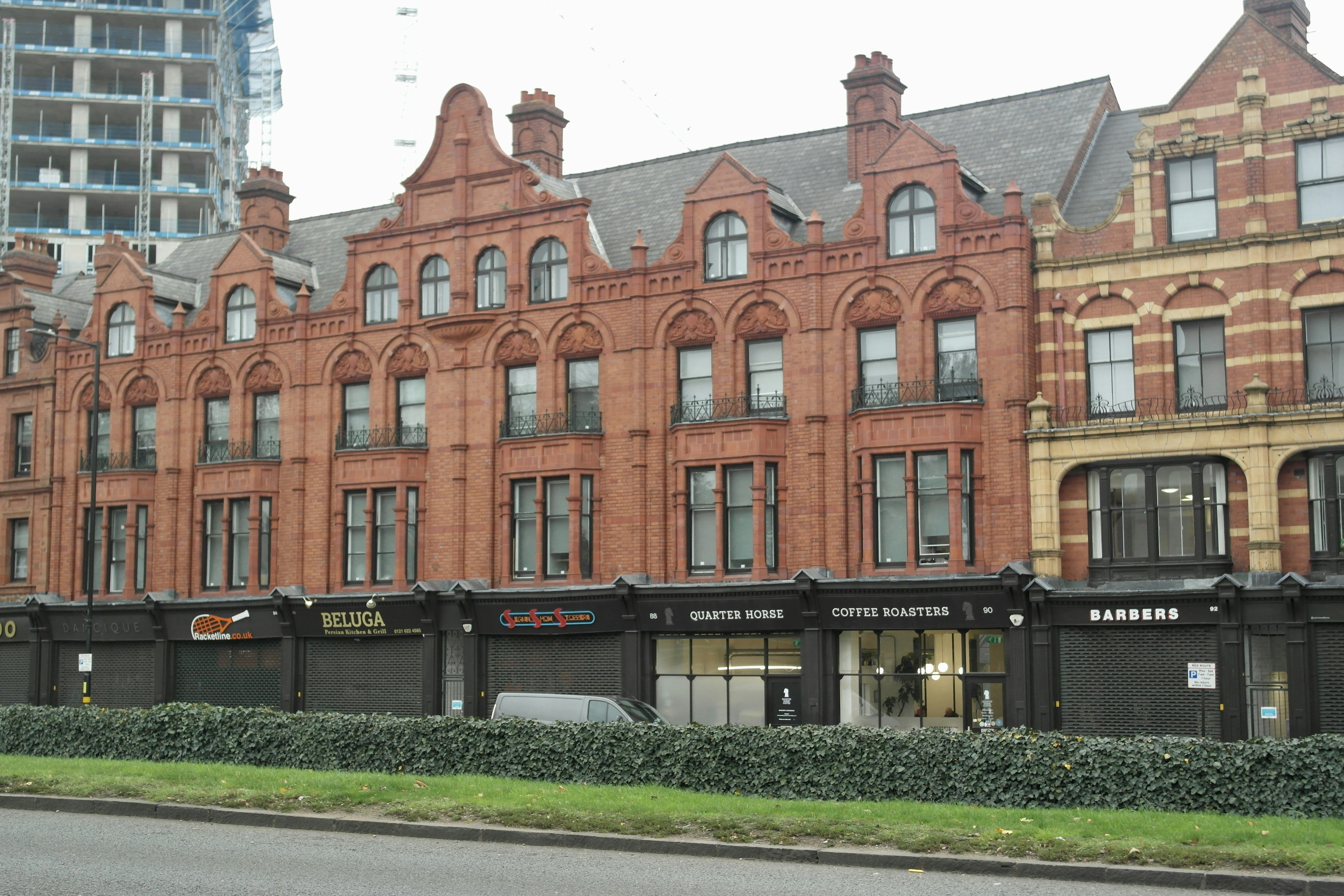 Historic red brick building with ornate gables and numerous windows, set against a backdrop of modern architecture.
