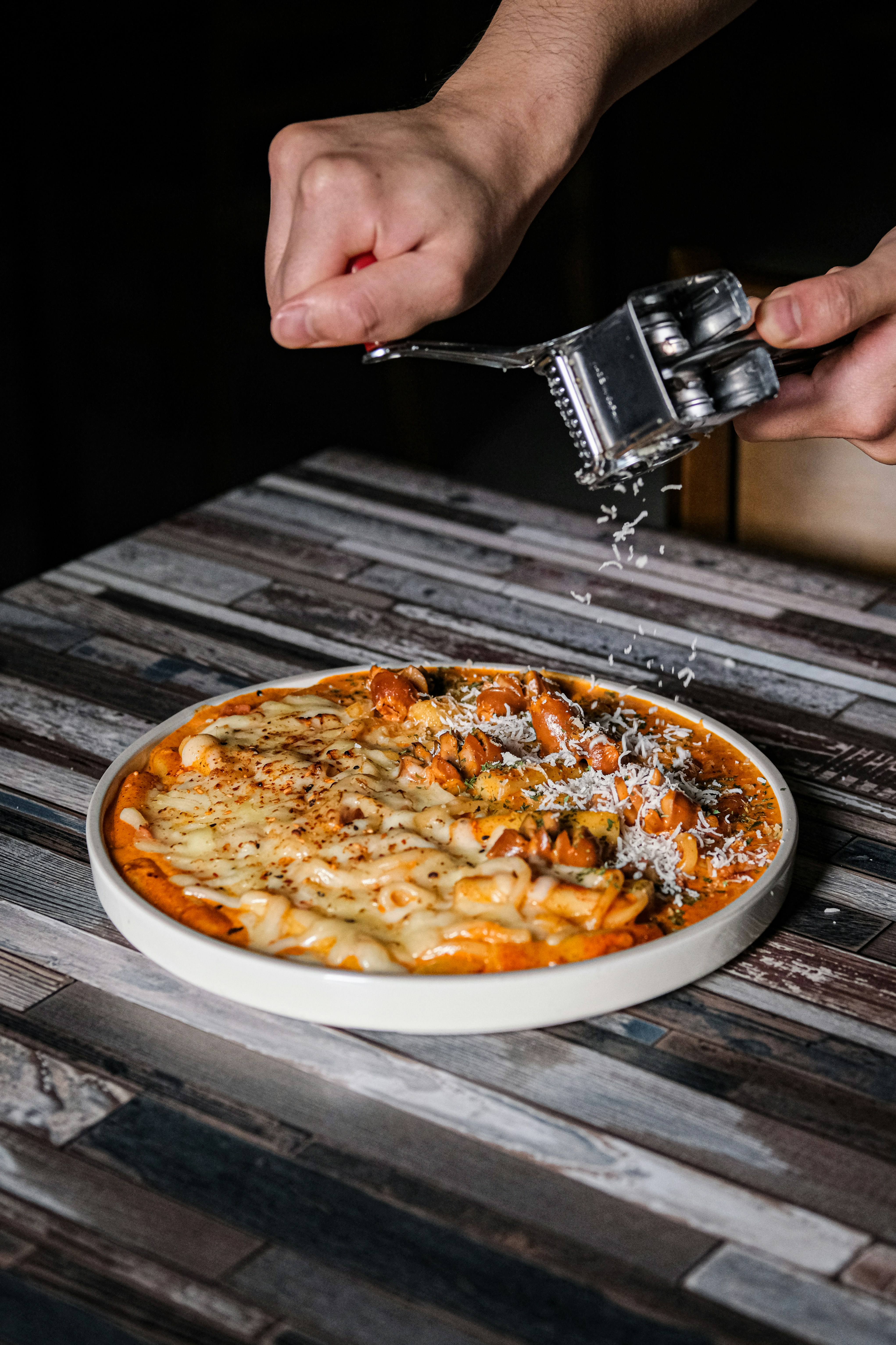 Grated cheese cascade over a bubbling skillet pizza being topped
