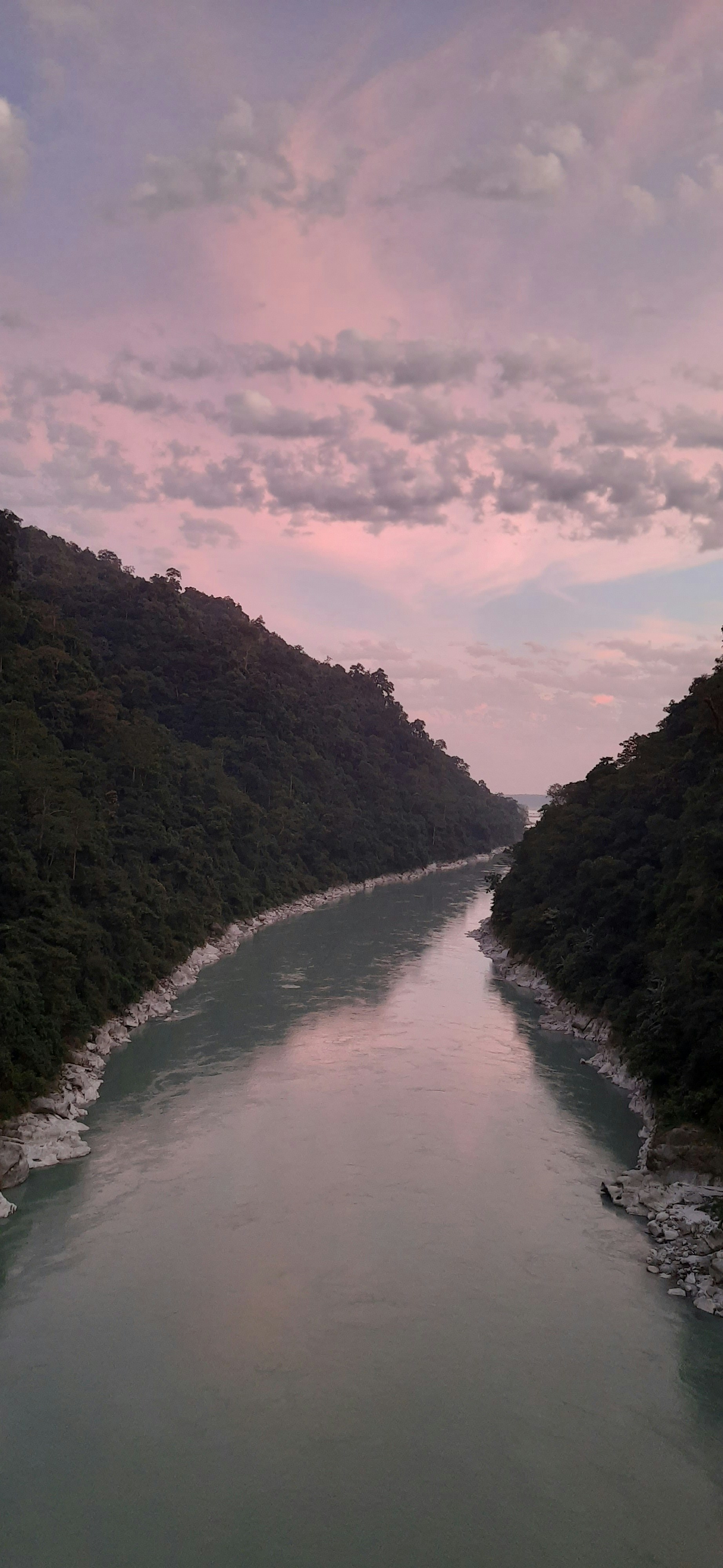 A winding river flows between lush green hills under a pastel sky, reflecting the soft hues of twilight.