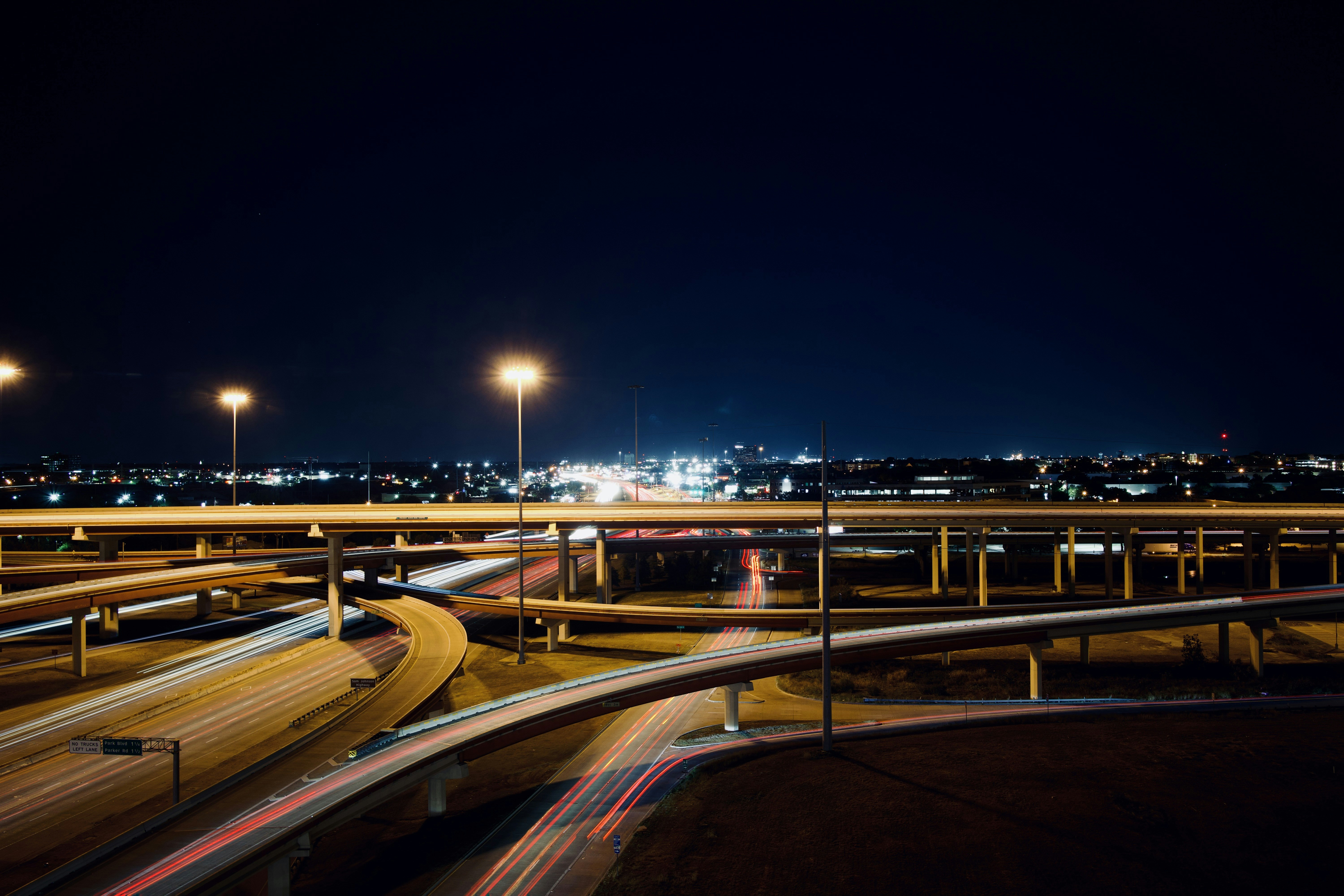 Highway interchange illuminated by streetlights, with streaking car lights against a city skyline at night.