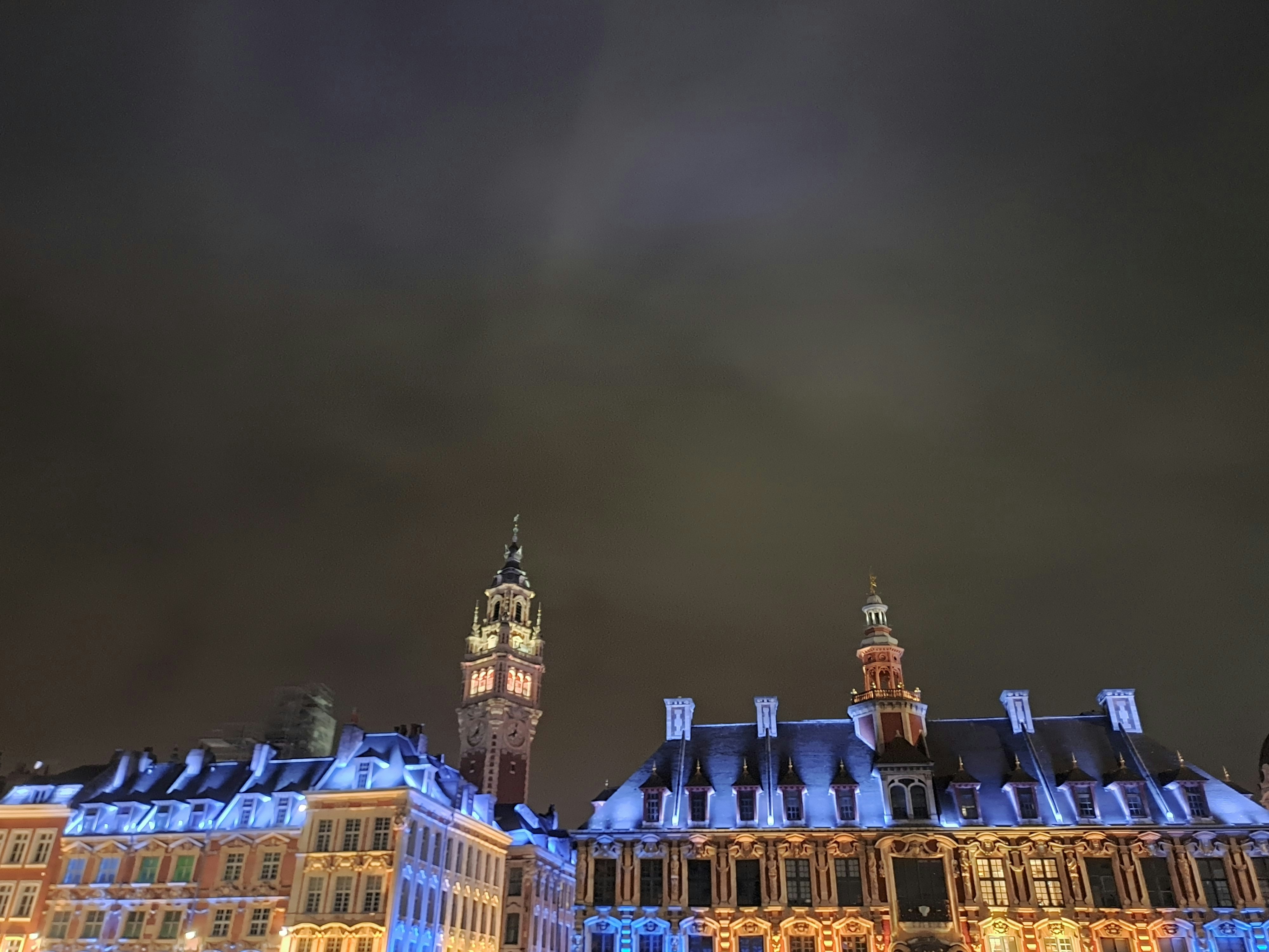 Historic building facades bathed in blue light under a cloudy night sky.