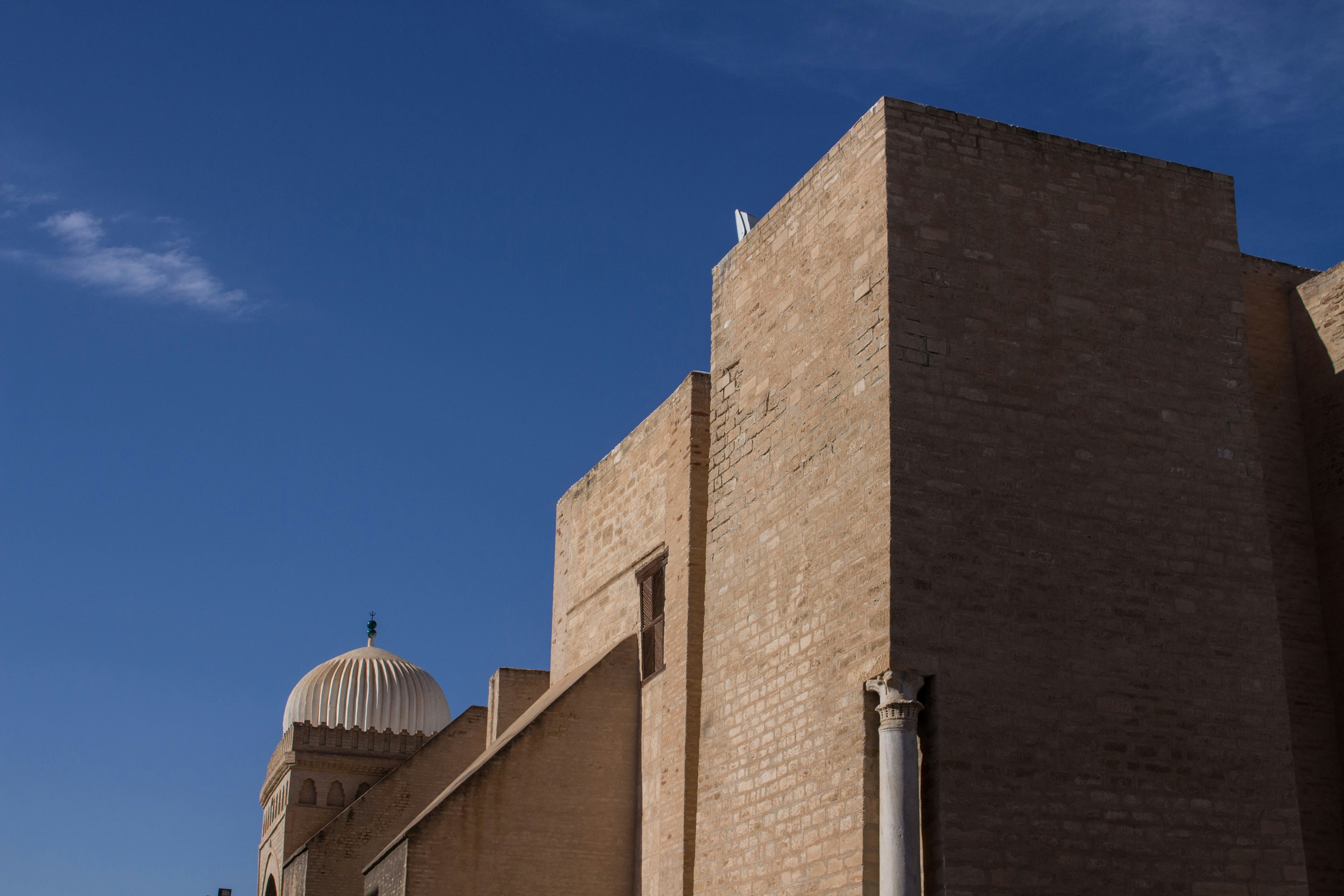 Sunlit brick walls and a domed structure against a clear blue sky.