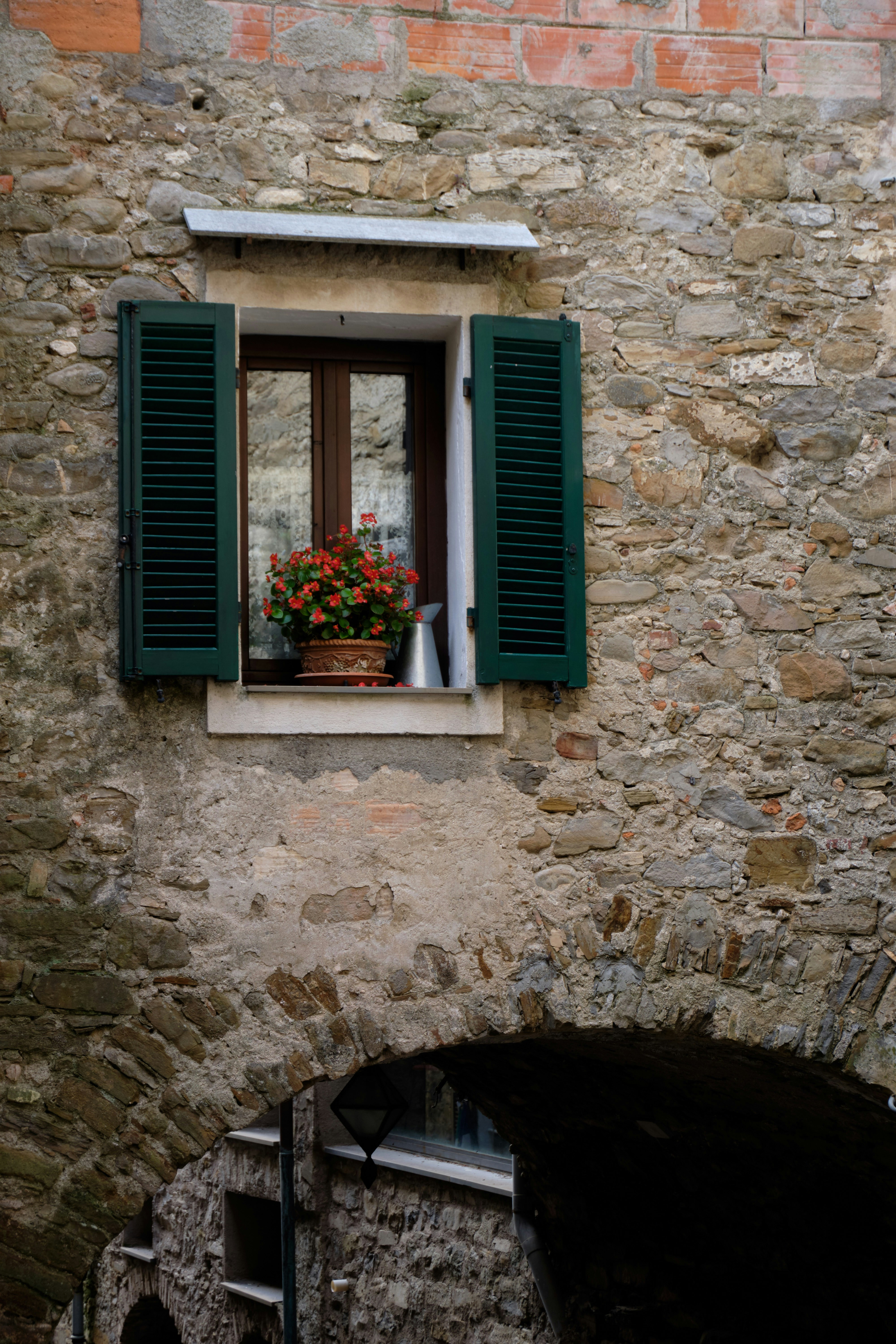 Crimson Geraniums Framed by Green Shutters on a Rustic Stone Façade