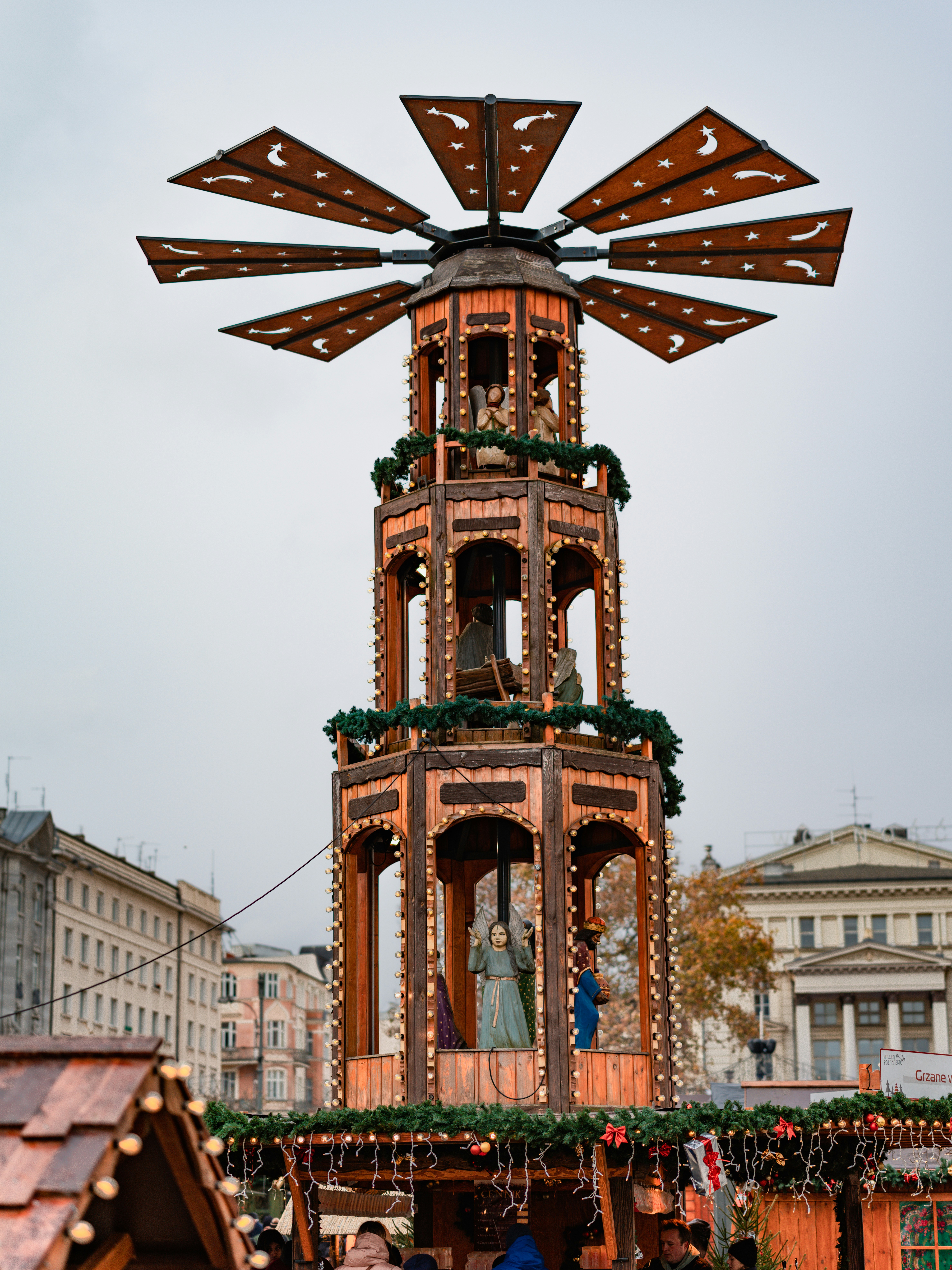 Intricately designed wooden carousel with festive decorations, featuring figurines and a starry canopy. Set against a soft gray sky.