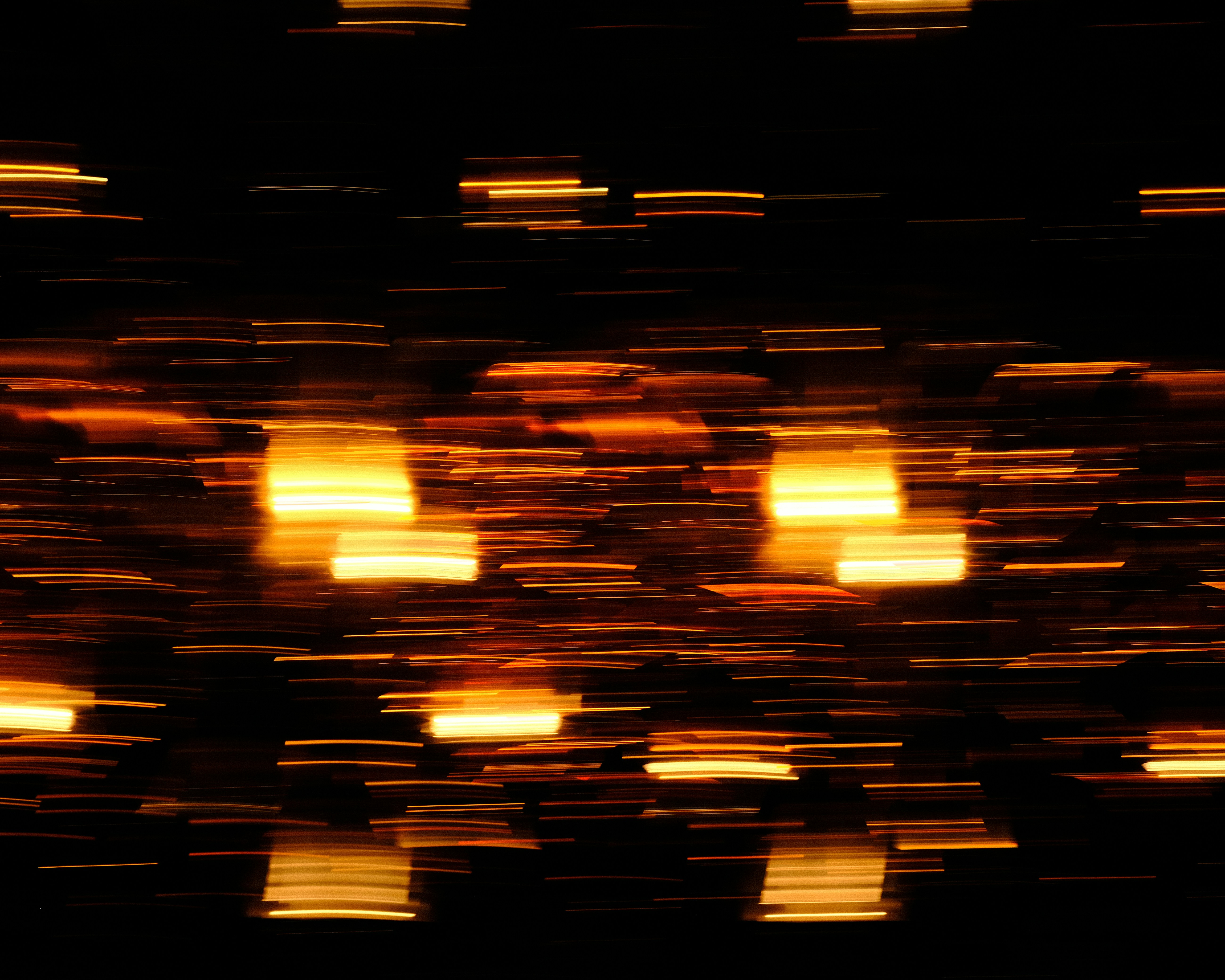 Abstract light trails created by moving lights against a dark backdrop, showcasing vibrant hues of orange and yellow.