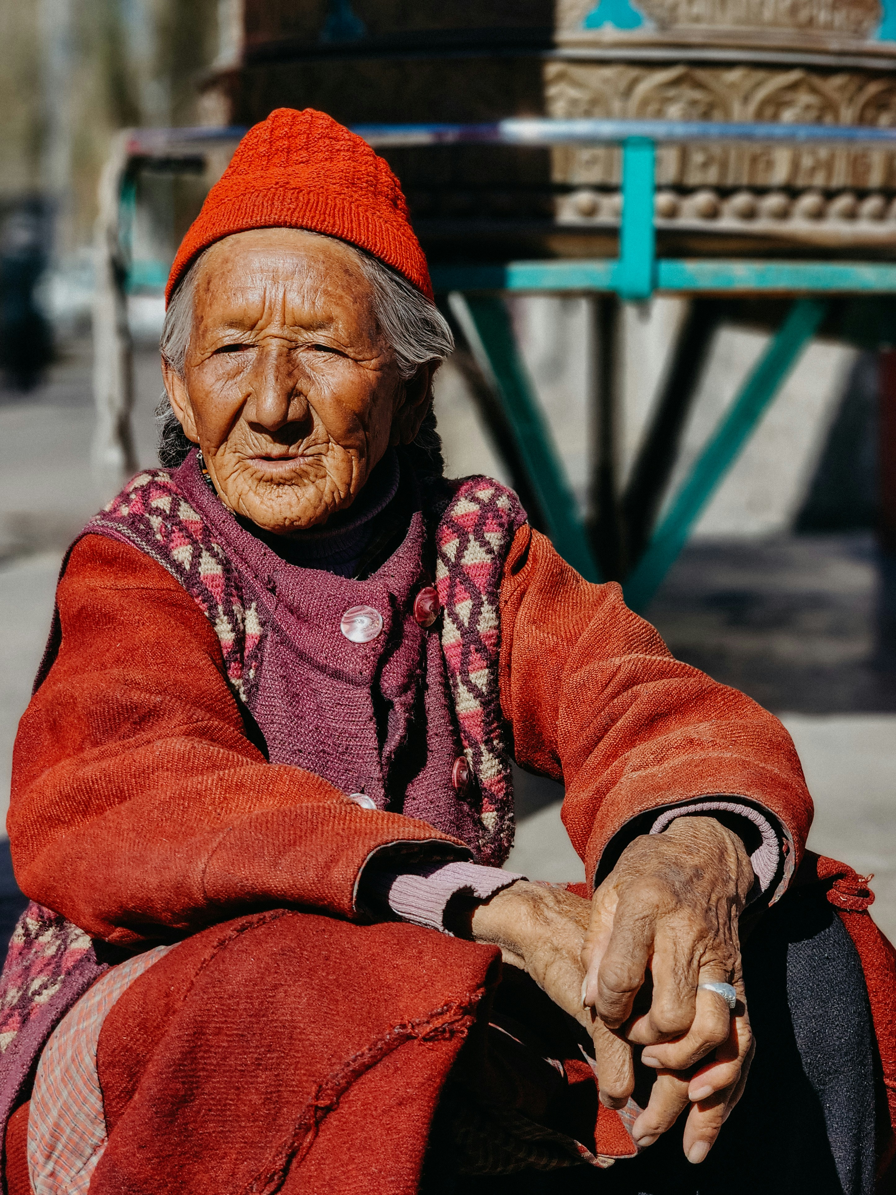 Elderly woman in vibrant traditional attire seated against a colorful background, exuding wisdom and strength.