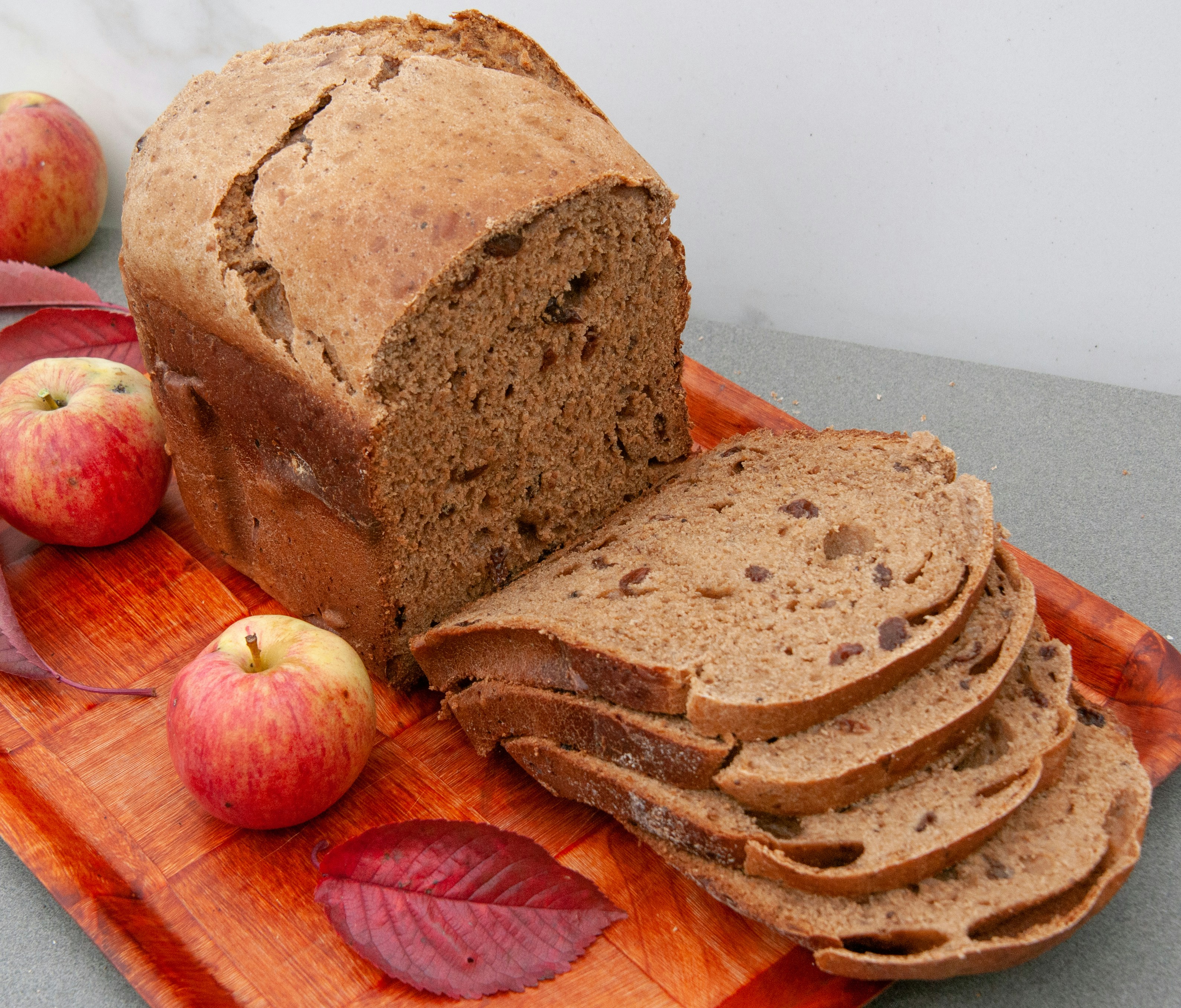 Brown loaf on a wooden board with red apples and a leaf