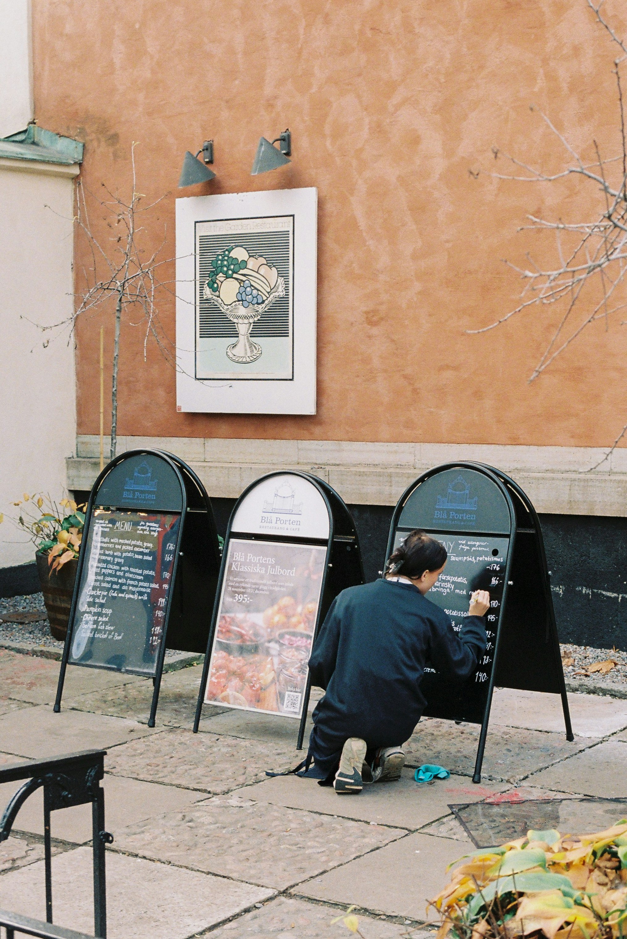 Kneeling Barista Drafts a Menu Under a Peach Wall