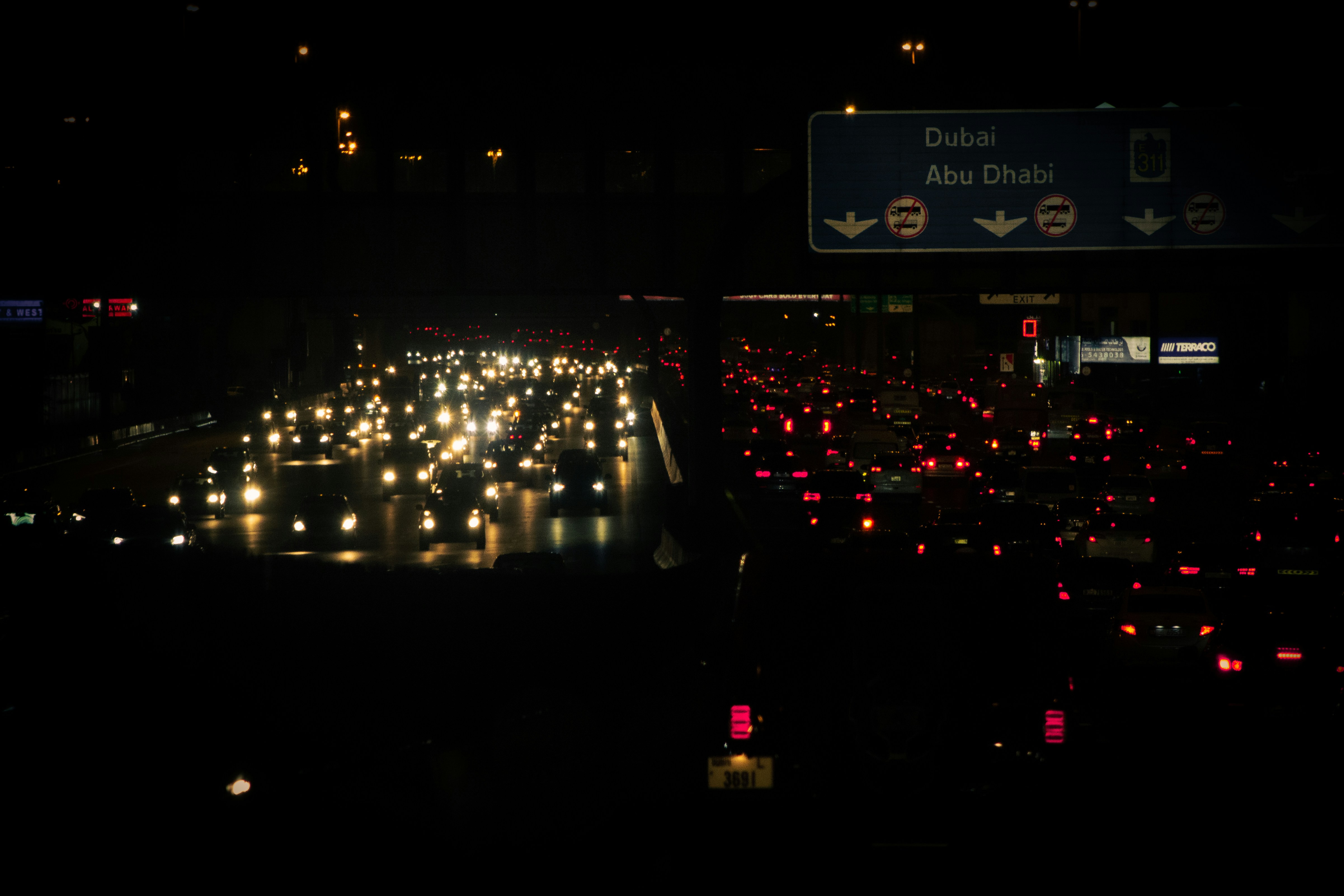 Converging Headlight Lanes Beneath Dubai's Night Sign