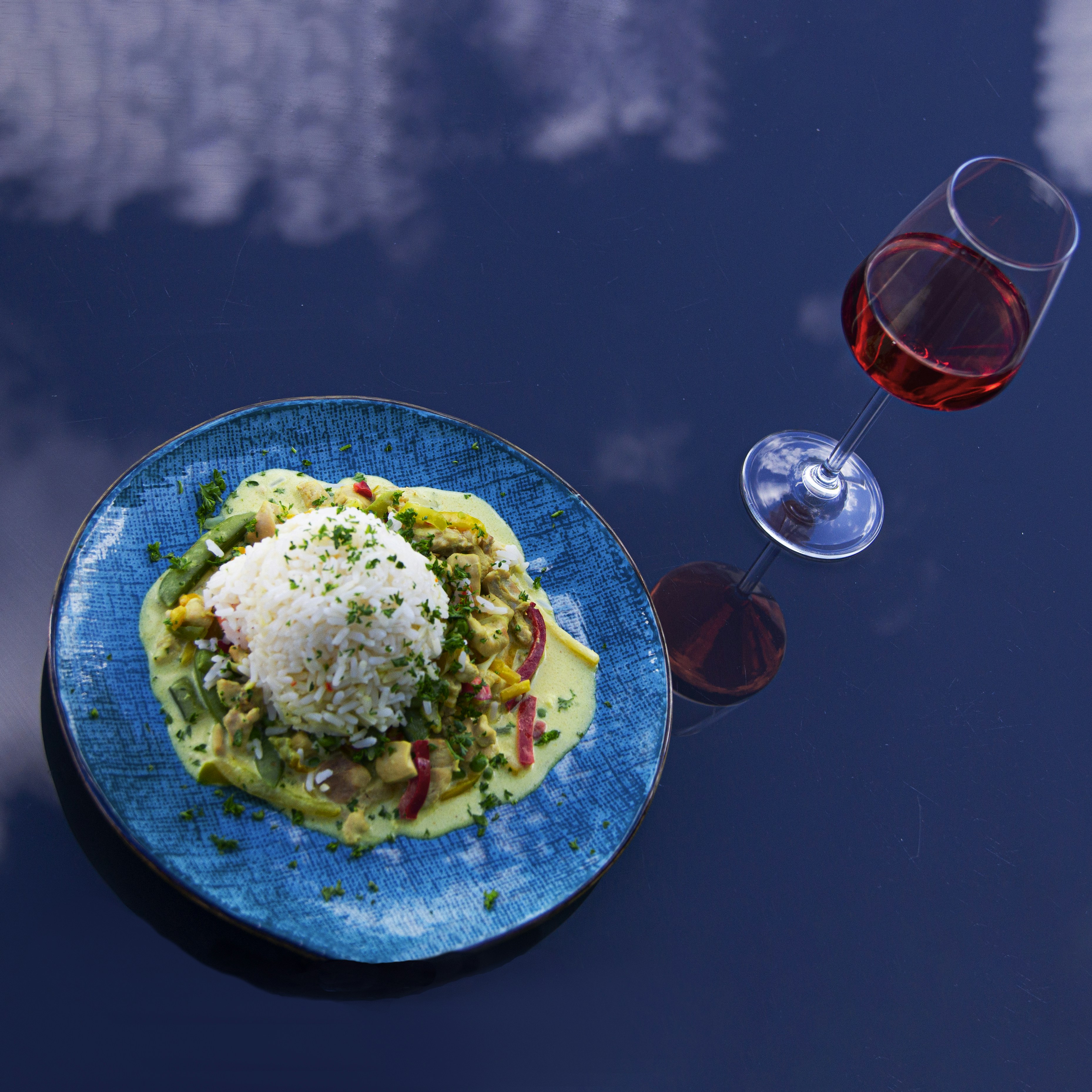 Vibrant plate featuring rice and mixed vegetables in a creamy sauce, accompanied by a glass of rosé wine. Reflections enhance the visual appeal.
