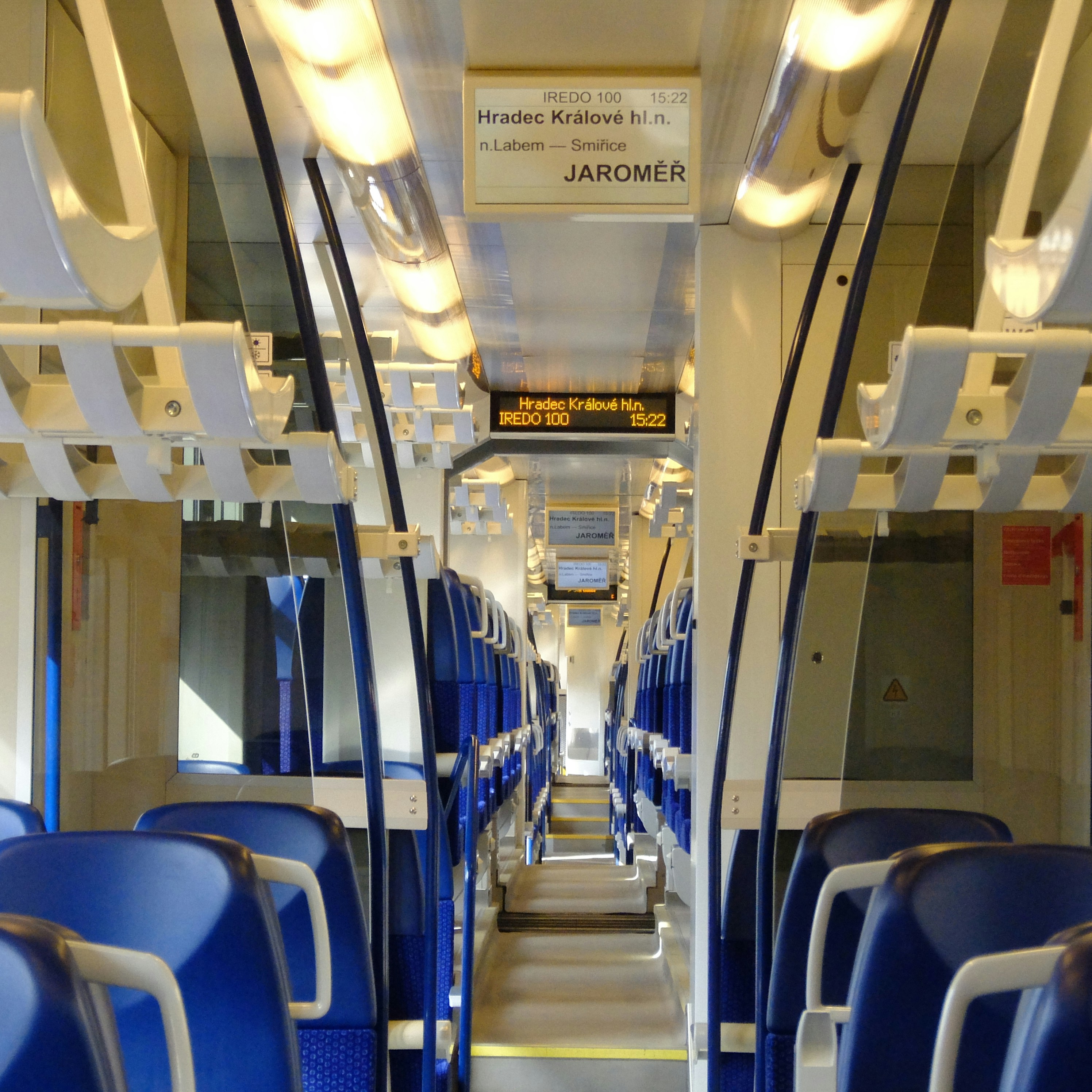 Photograph of a modern train carriage interior with blue seats and overhead signage, viewed along the central aisle.