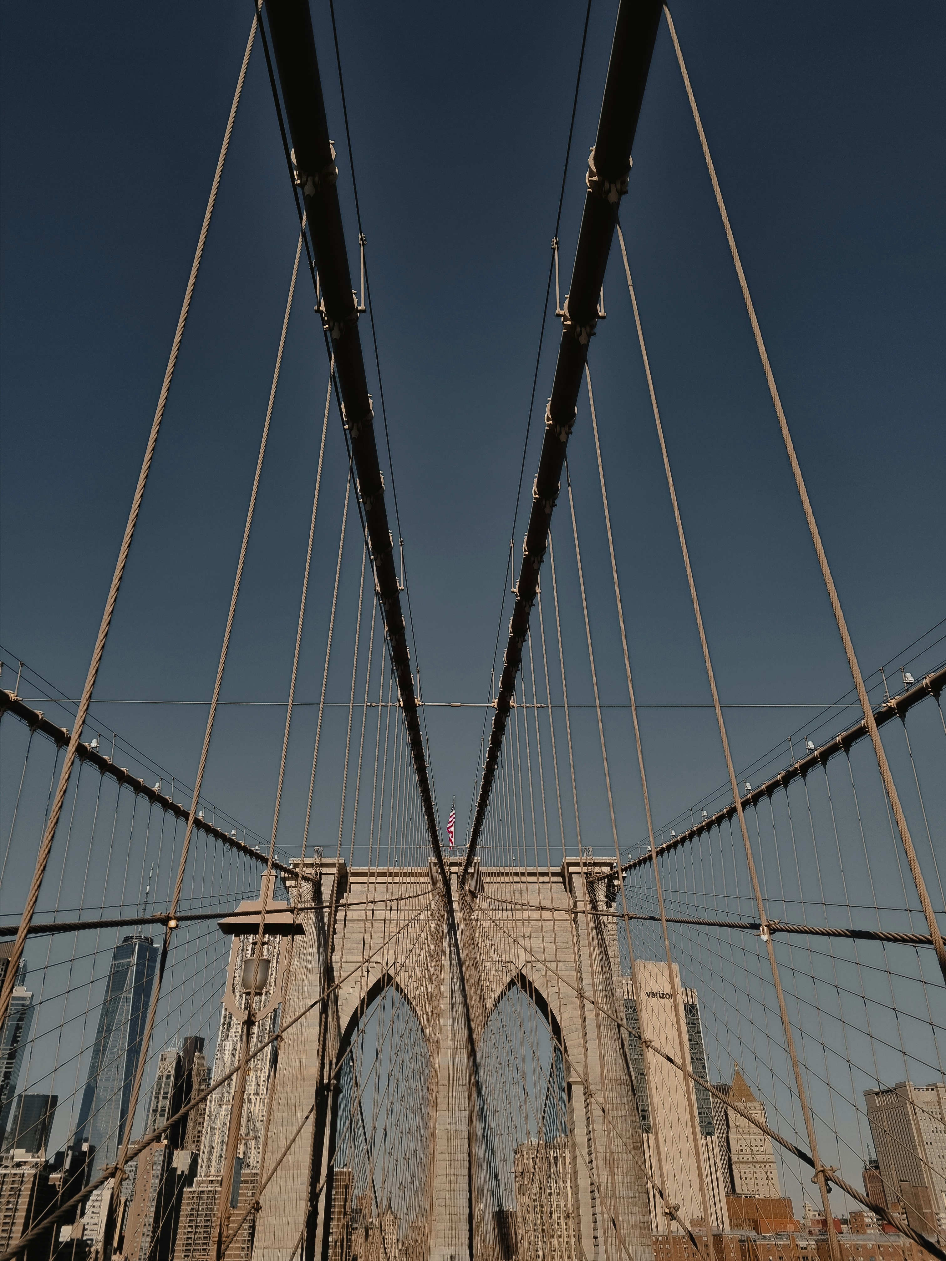 Brooklyn Bridge captured from below, showcasing its intricate cables and arches against a clear blue sky.