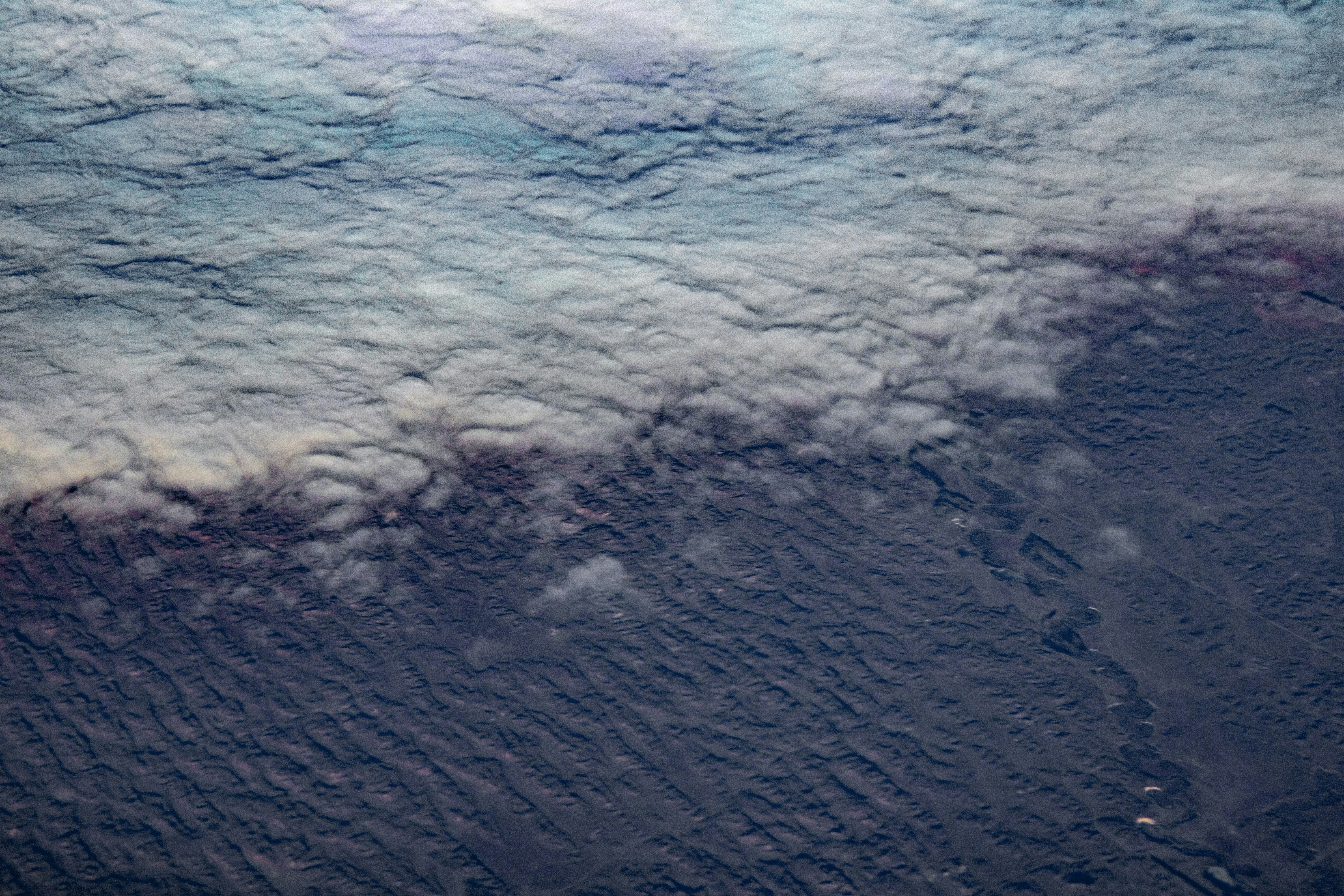 Aerial view showcasing textured cloud formations merging with the earth's surface, highlighting the interplay between atmospheric and terrestrial elements.