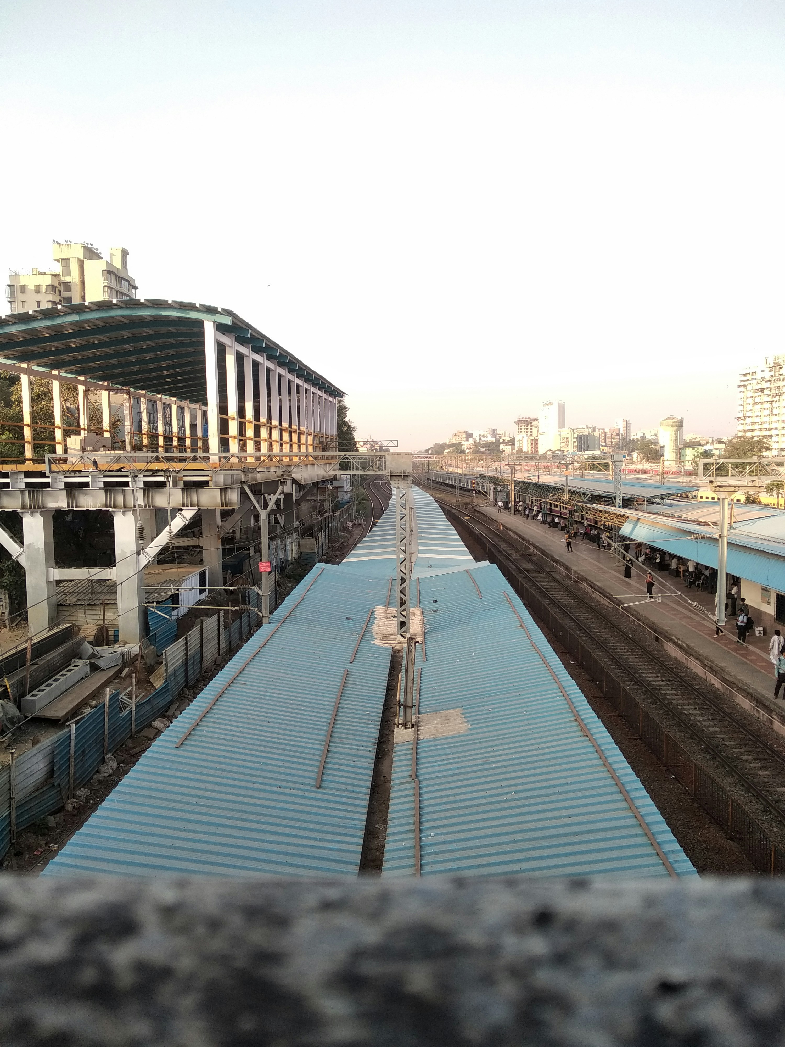 Railway station with blue roofs and tracks extending into the distance, showcasing urban infrastructure and transit activity.
