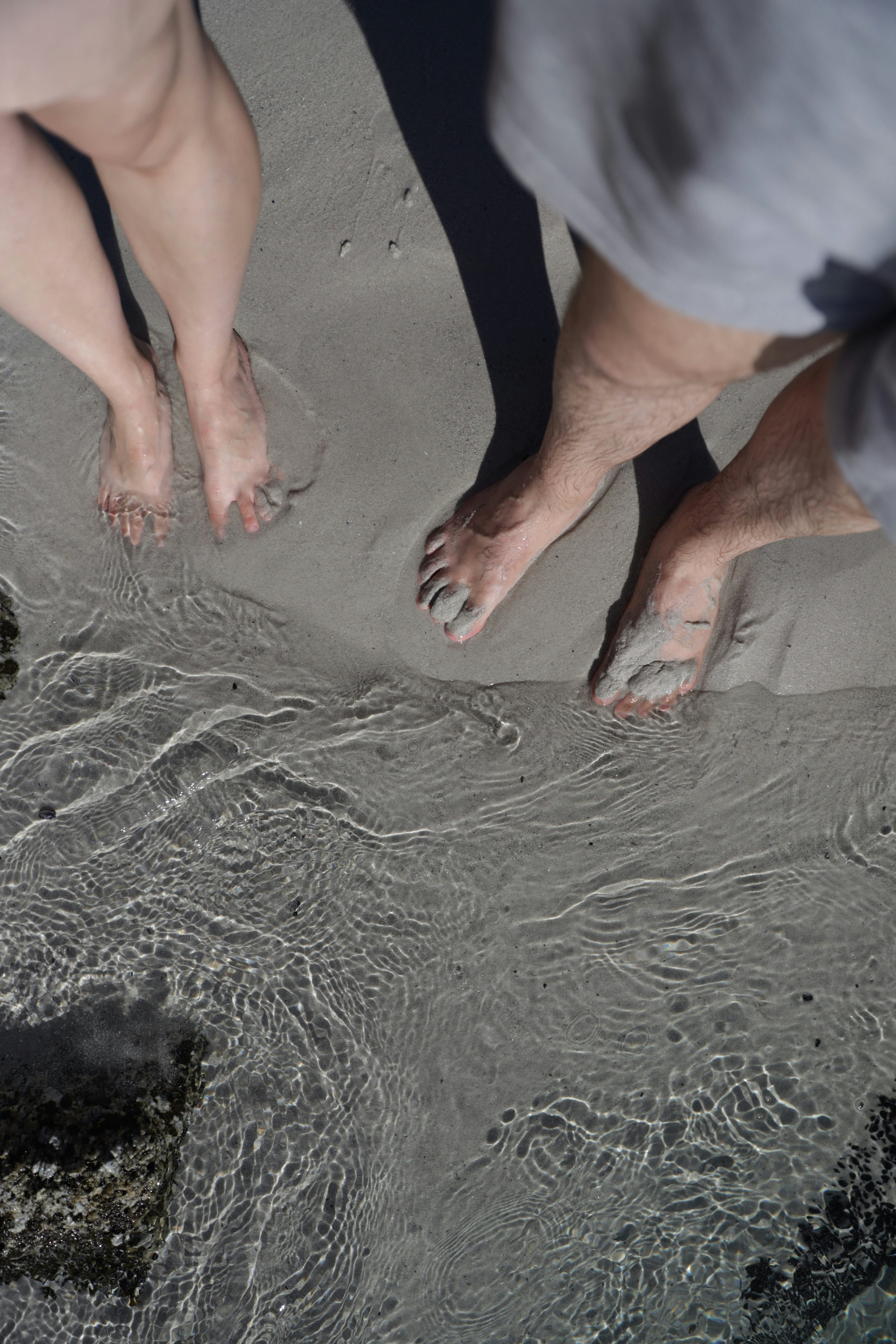 Two pairs of feet wade through gentle waves on a sandy beach, capturing a serene moment of connection with nature.