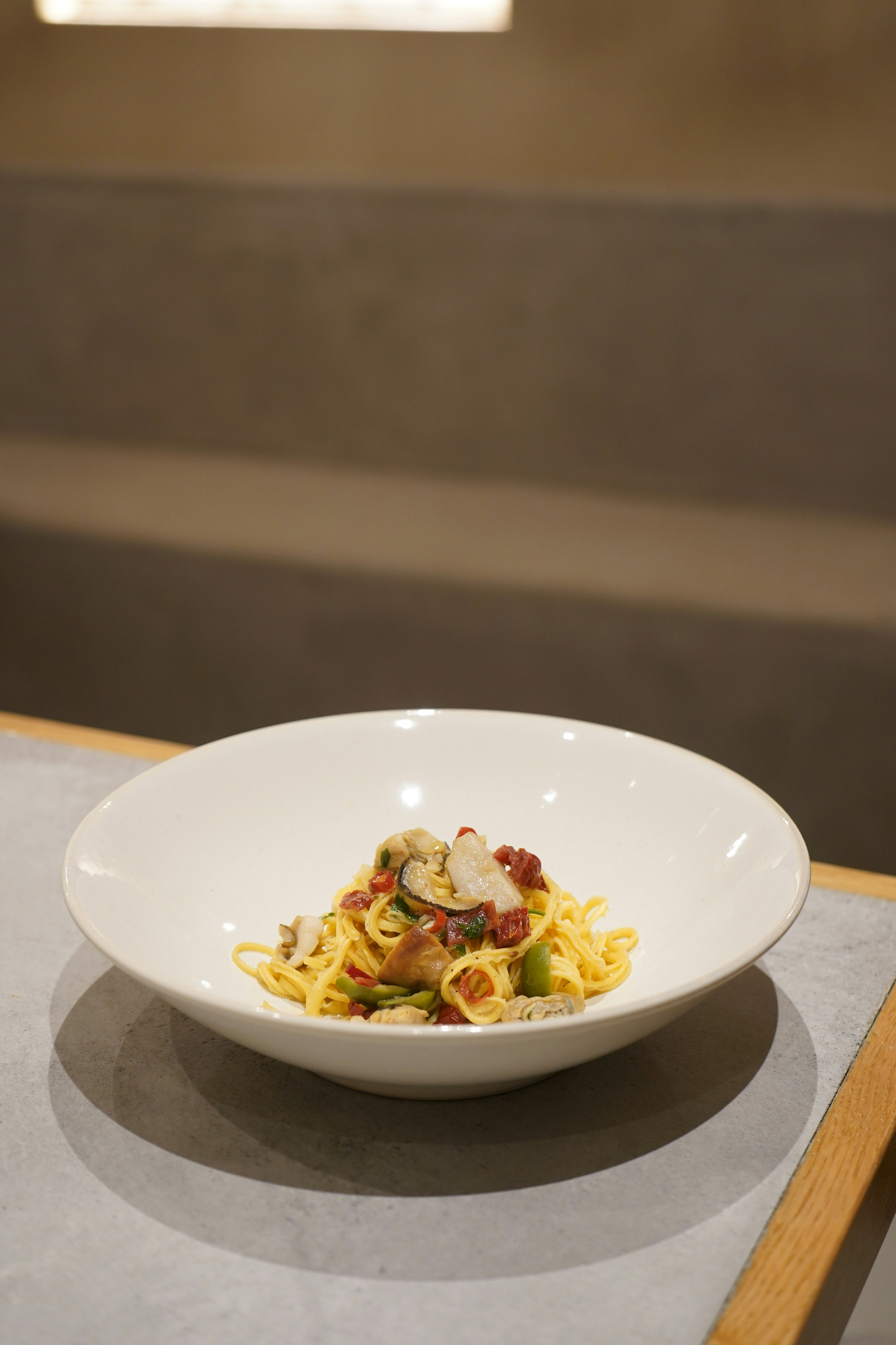 A beautifully plated pasta dish featuring strands of noodles topped with fresh seafood and vibrant vegetables. The minimalistic setting enhances the dish's appeal.