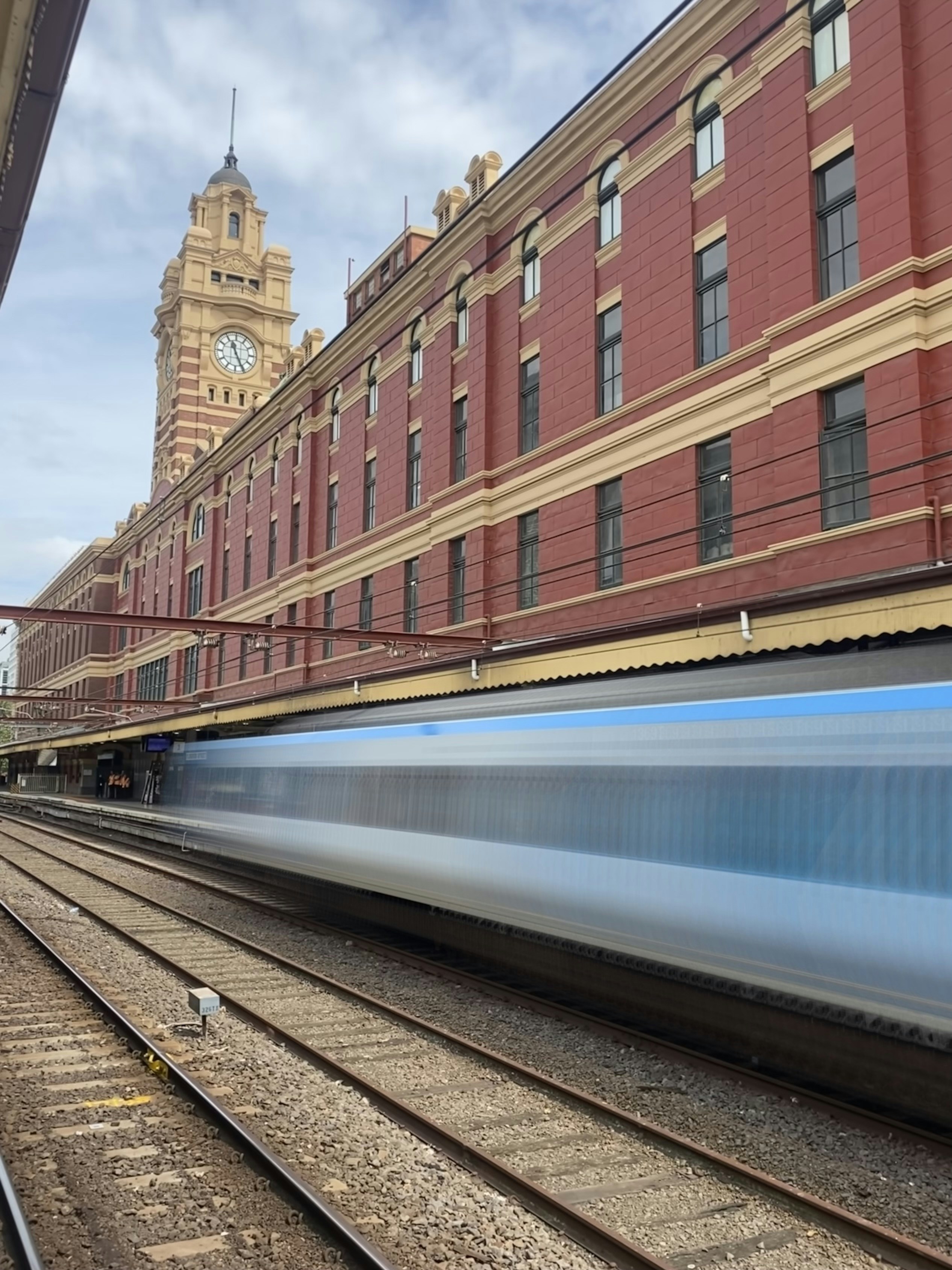 Clock Tower and Blue Train Slice Through a Red-Brick Station