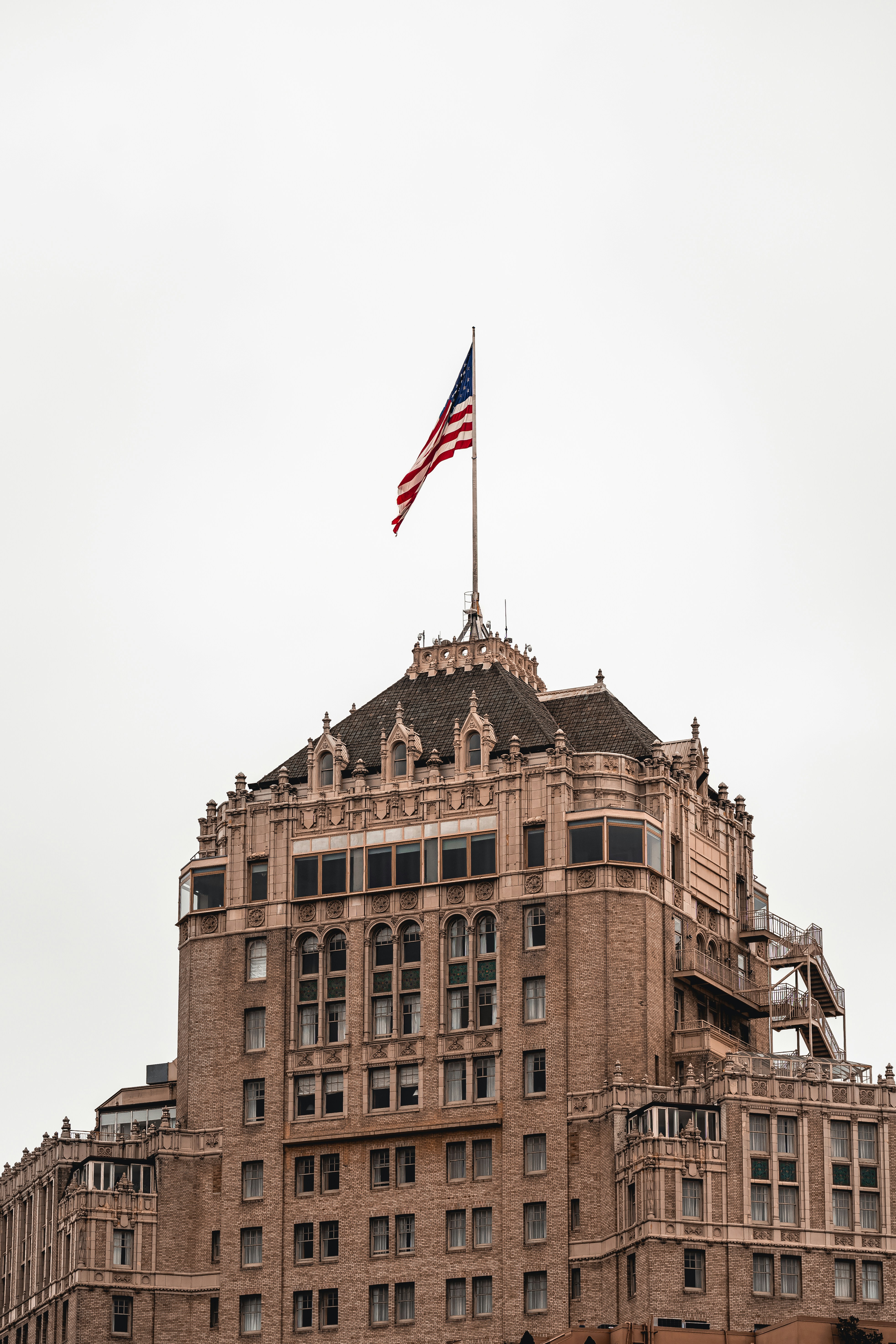 Tall historic building with intricate architecture topped by an American flag against a cloudy sky.
