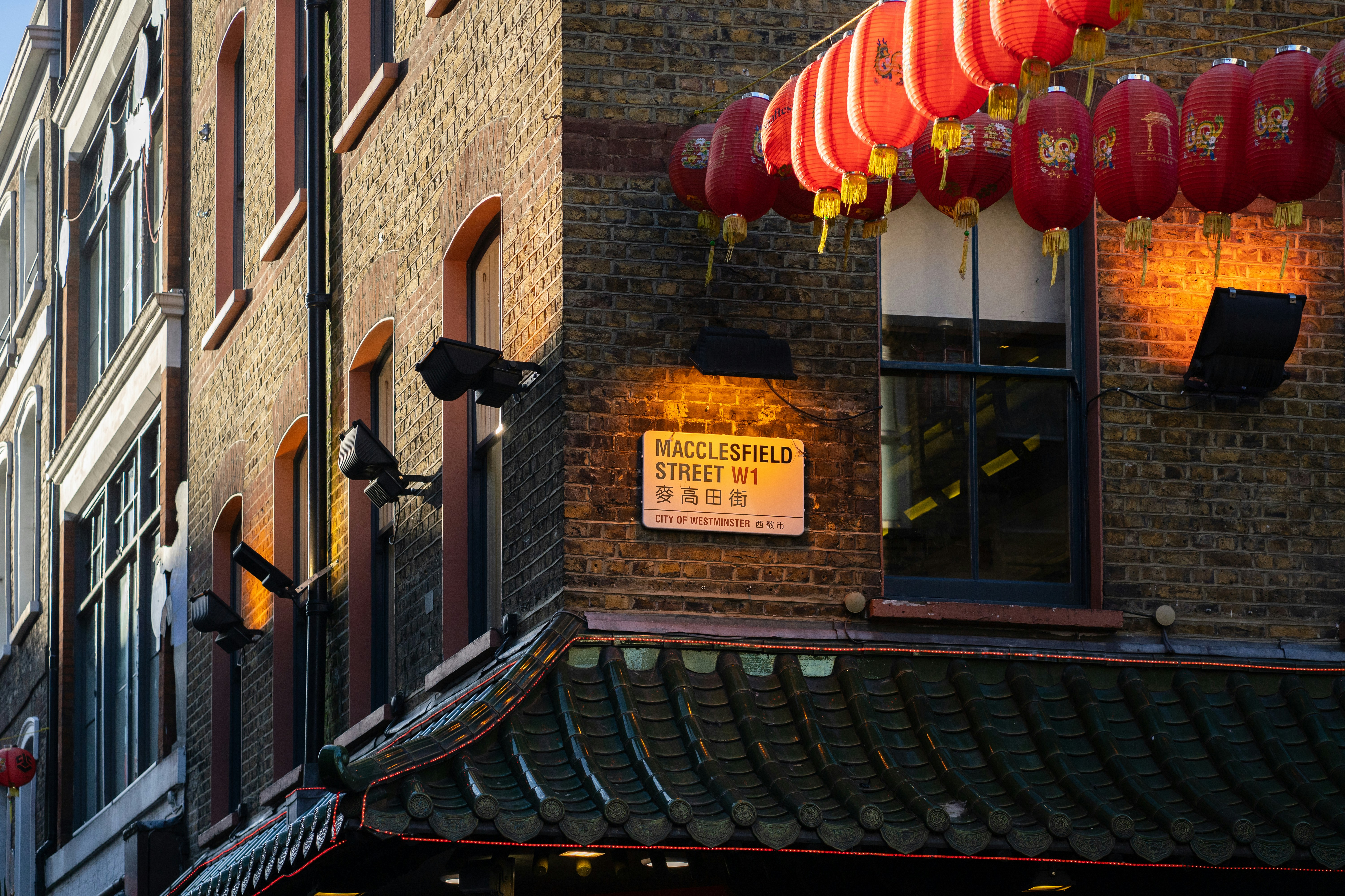 Macclesfield Street Sign Under a Lantern-Studded Brick Facade