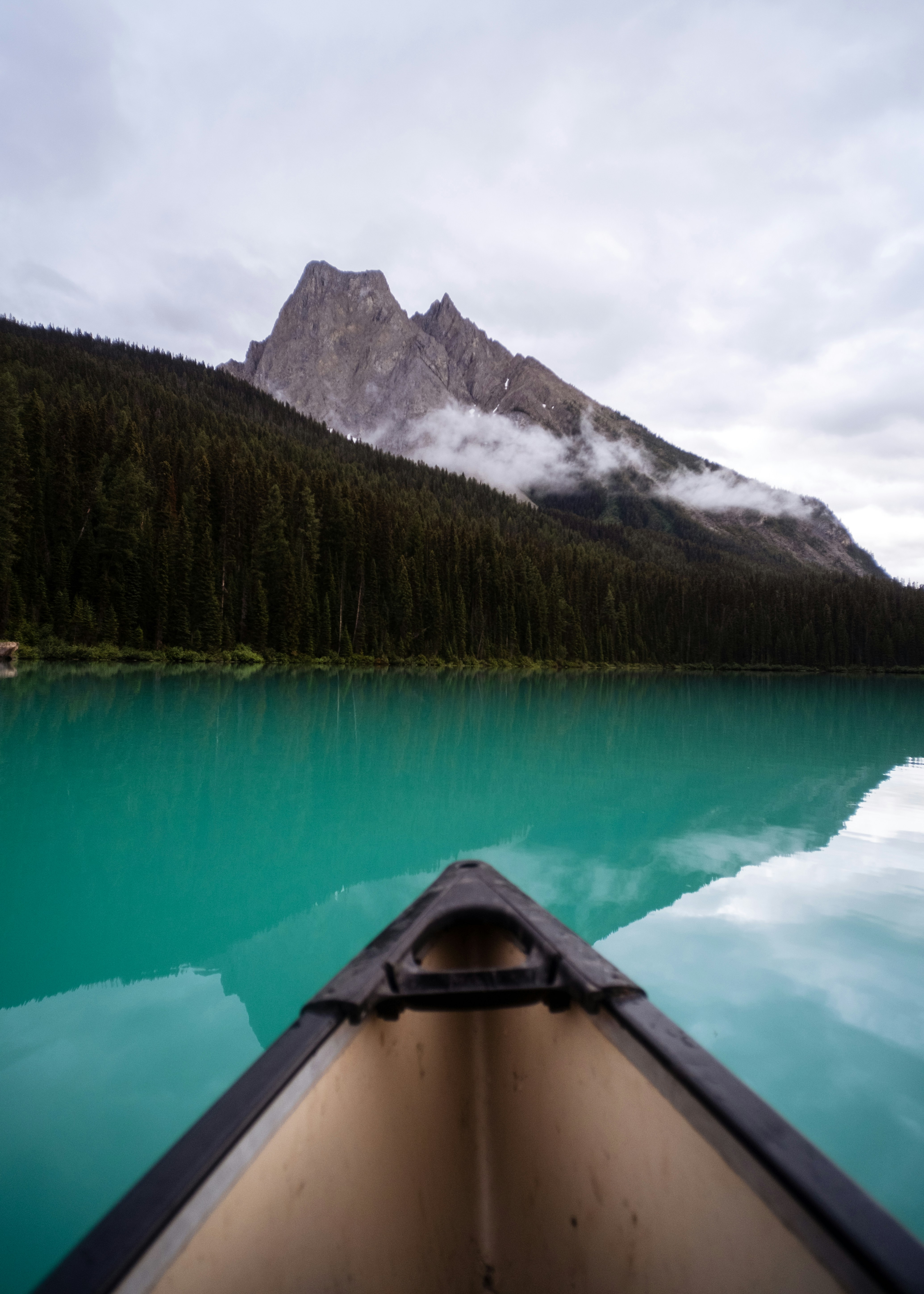 Canoe gliding across turquoise waters with a backdrop of towering mountains and lush forests, creating a serene atmosphere.