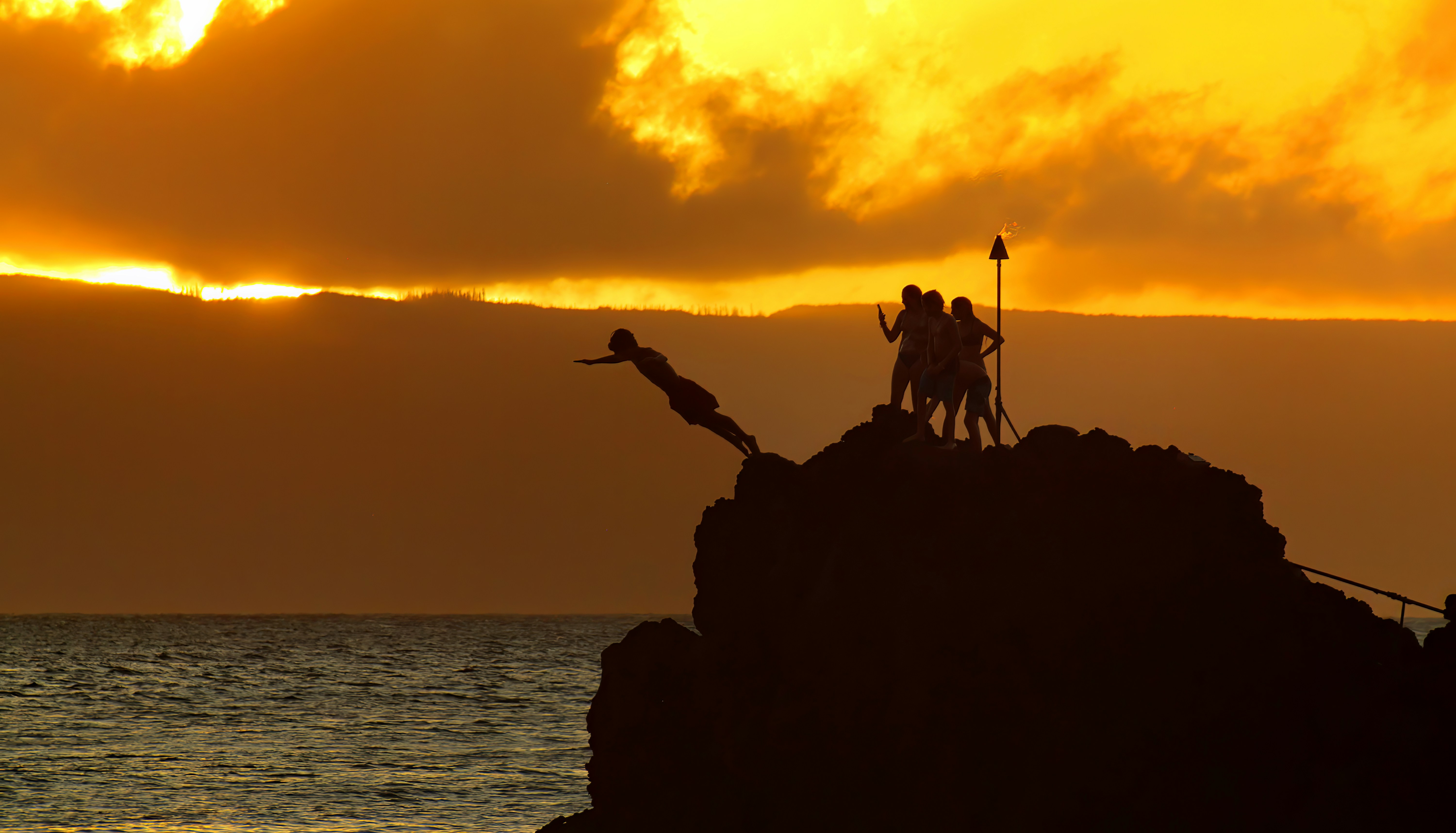 Golden-hour arc: silhouettes on a rocky promontory during sunset