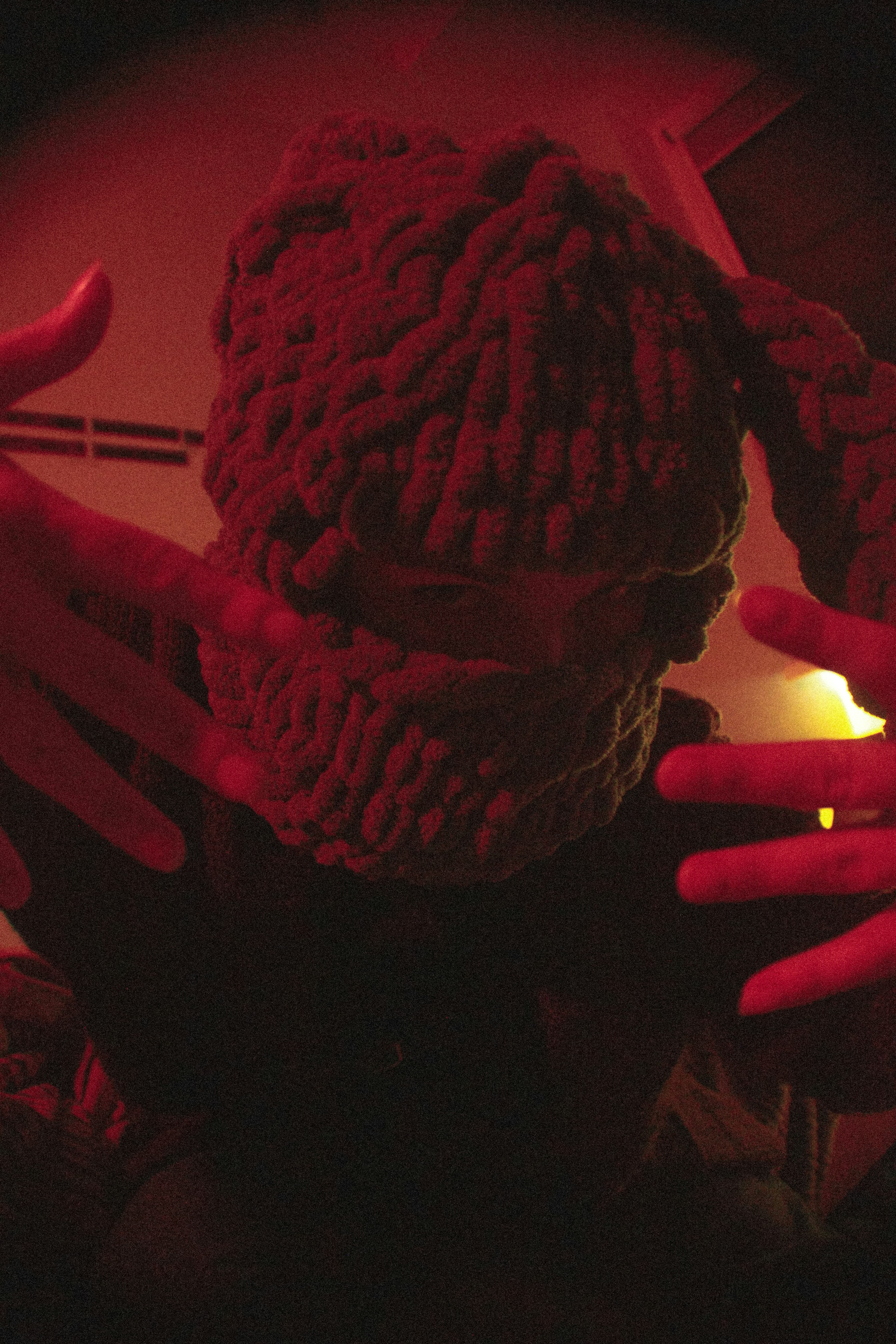 Crimson Shroud: A Knit-Masked Portrait Framed by Hands