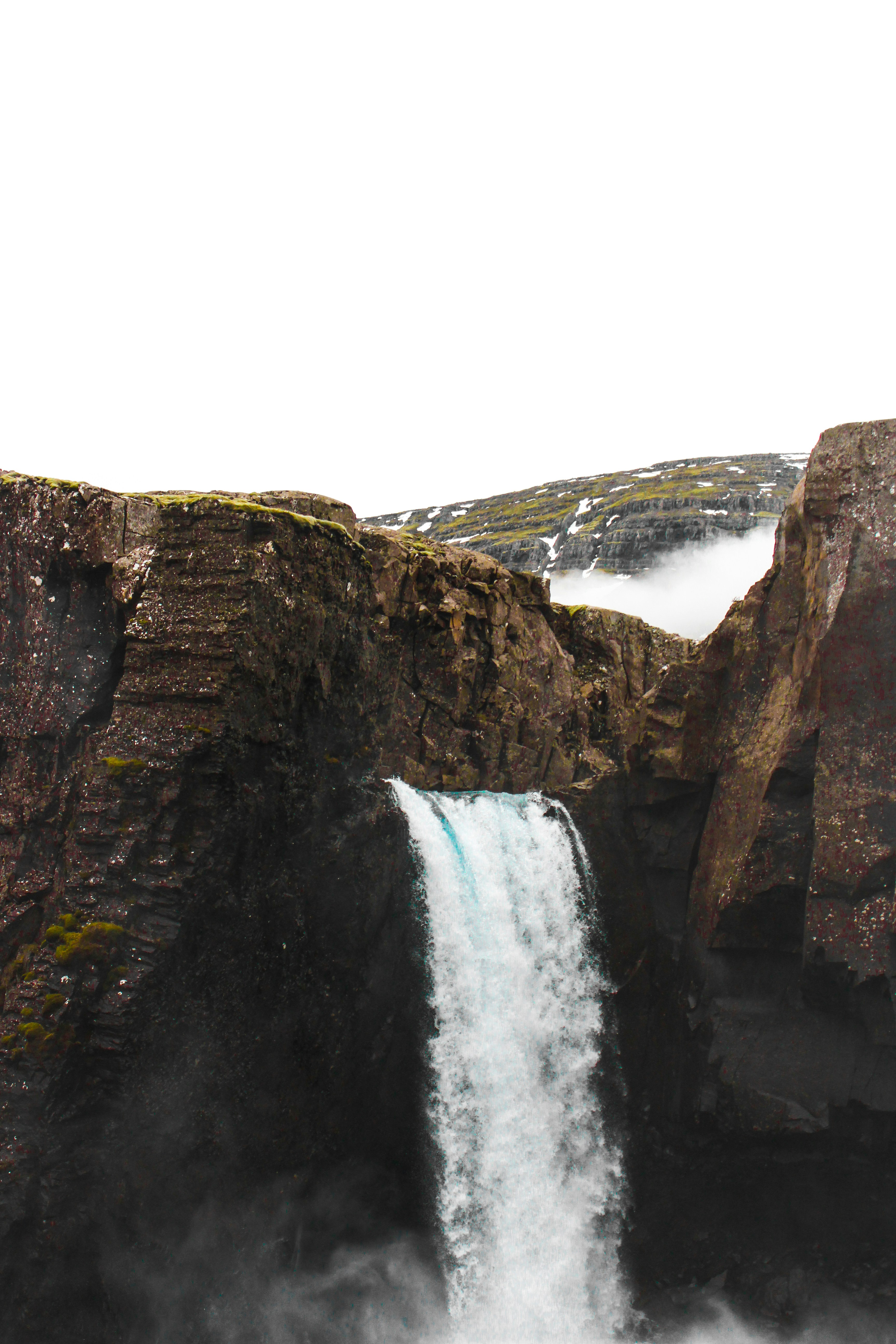 Majestic waterfall cascading over rugged cliffs, surrounded by mist and green moss. The scene captures the raw beauty of untouched wilderness.