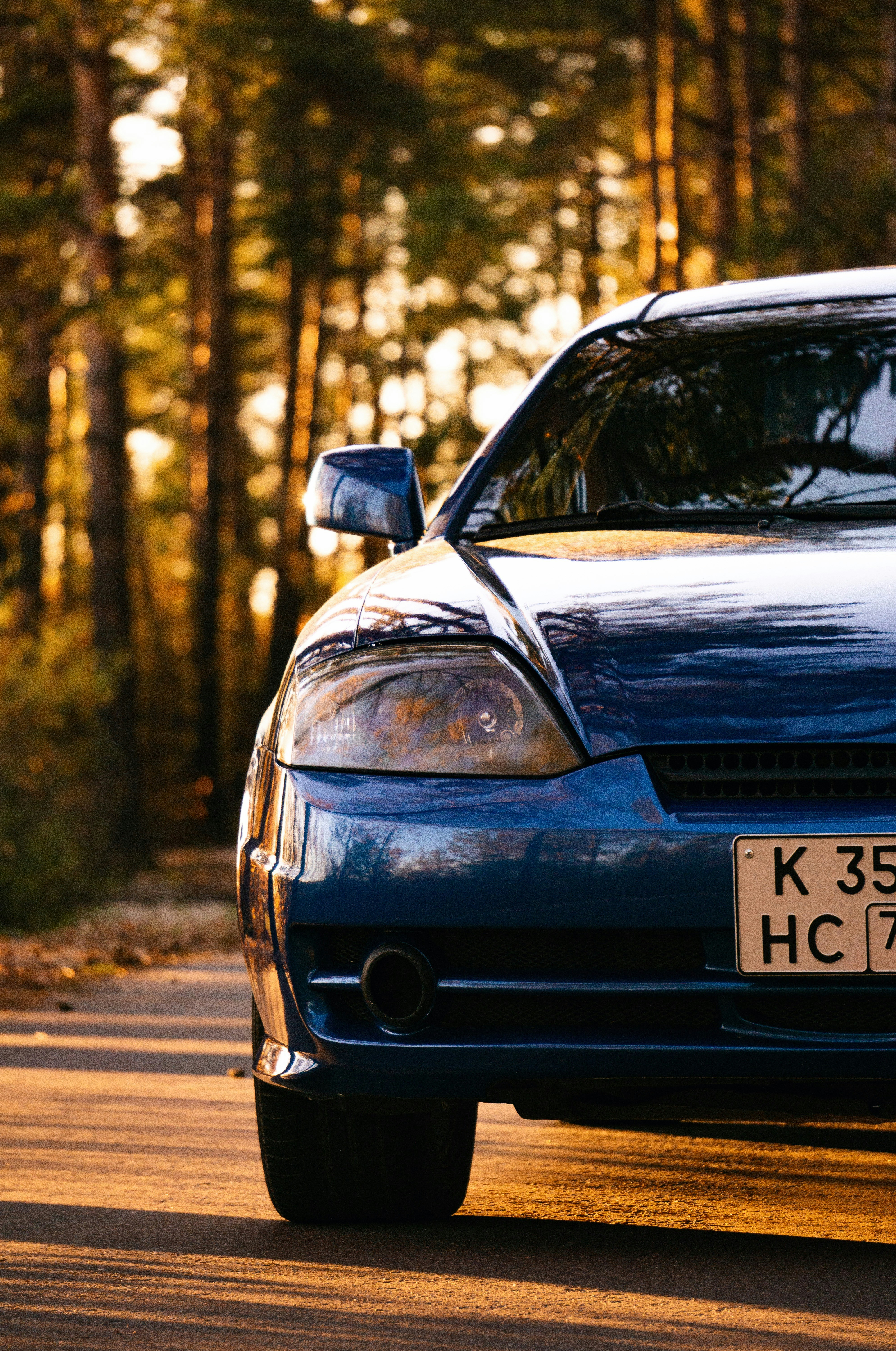 Blue Sedan in Golden Hour: Front View on a Quiet Forest Road