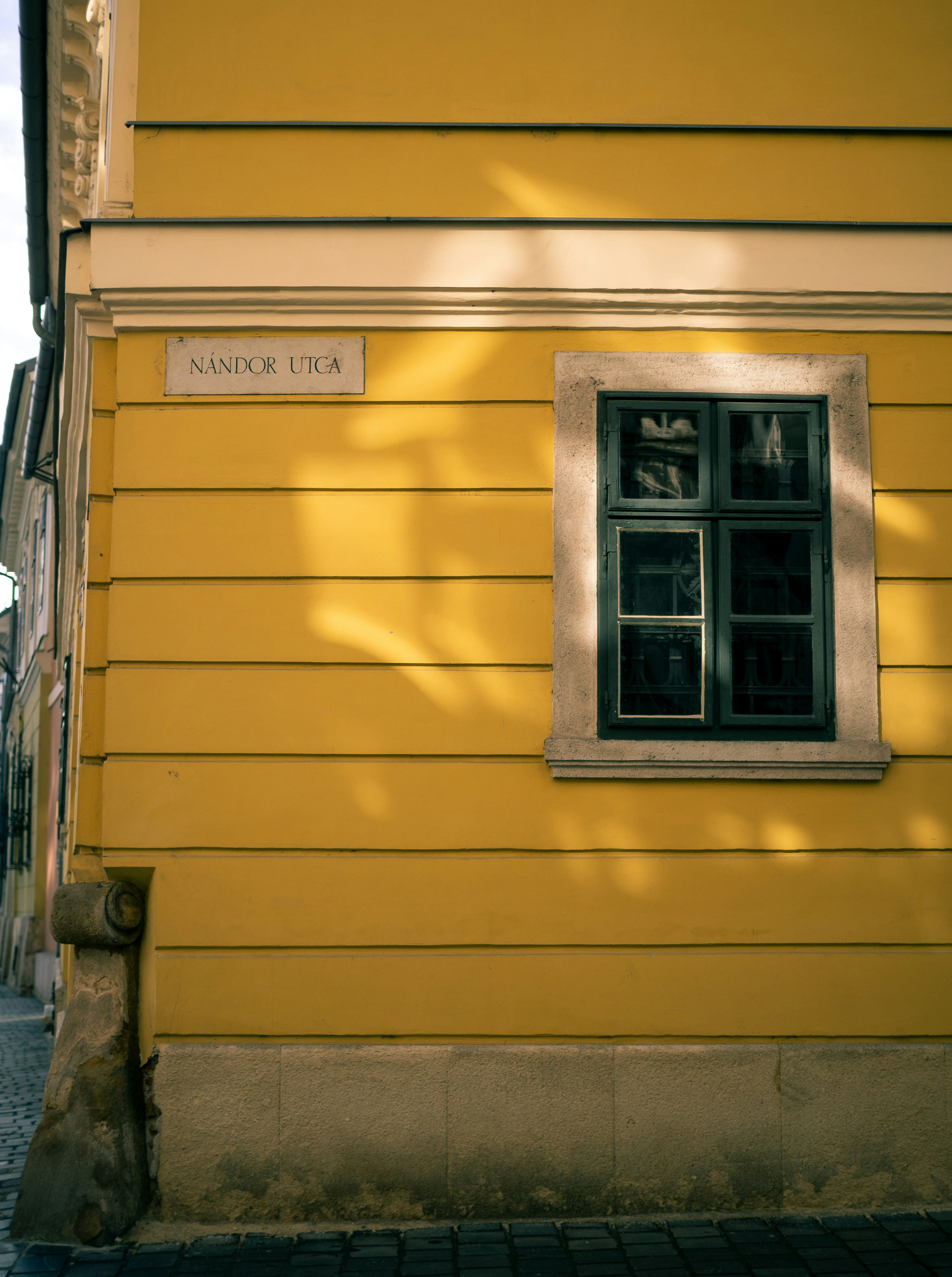 Sunlit window on Nándor utca's yellow facade, framed in green