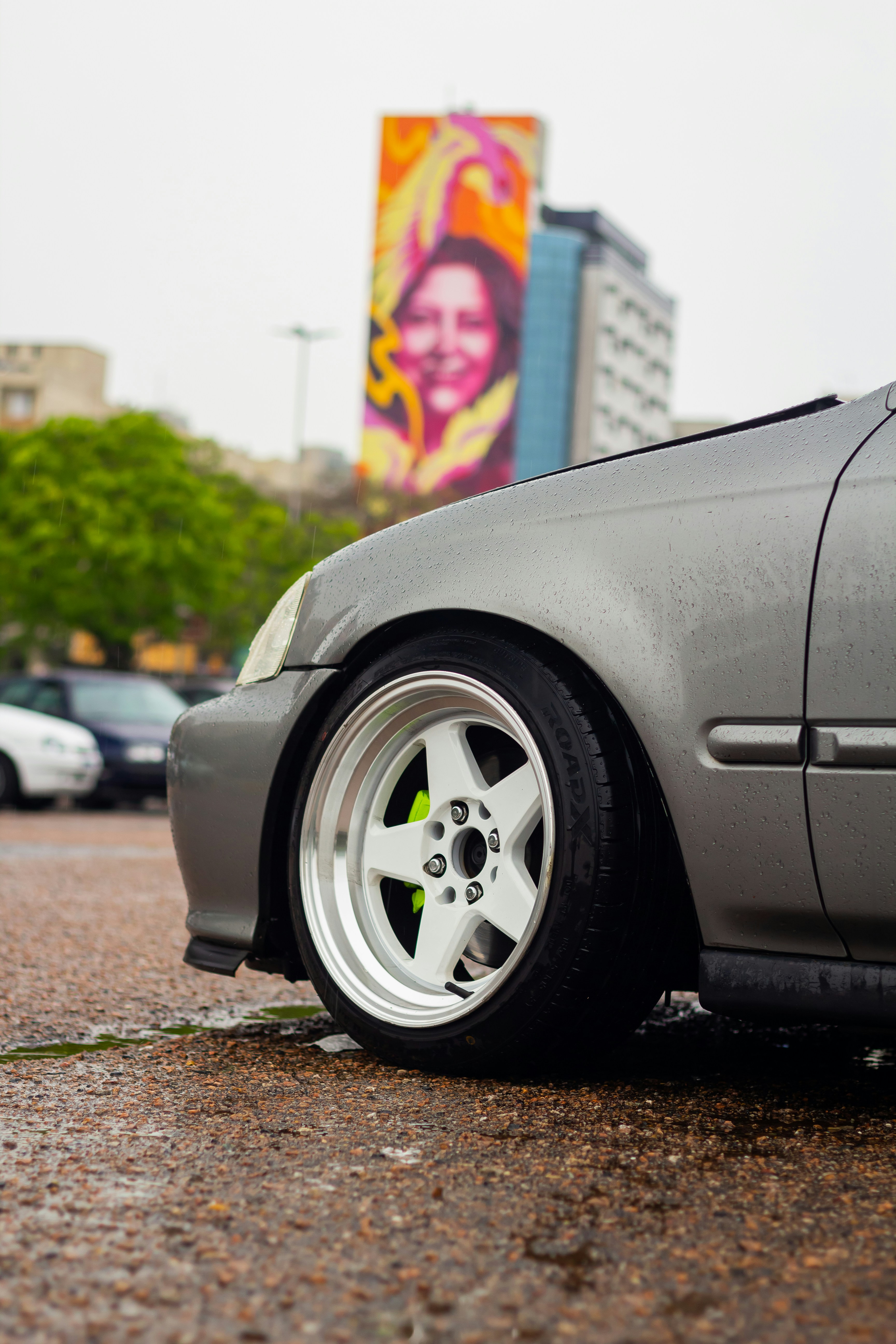 Low-angle street chrome: a close-up of a silver coupe against a mural backdrop