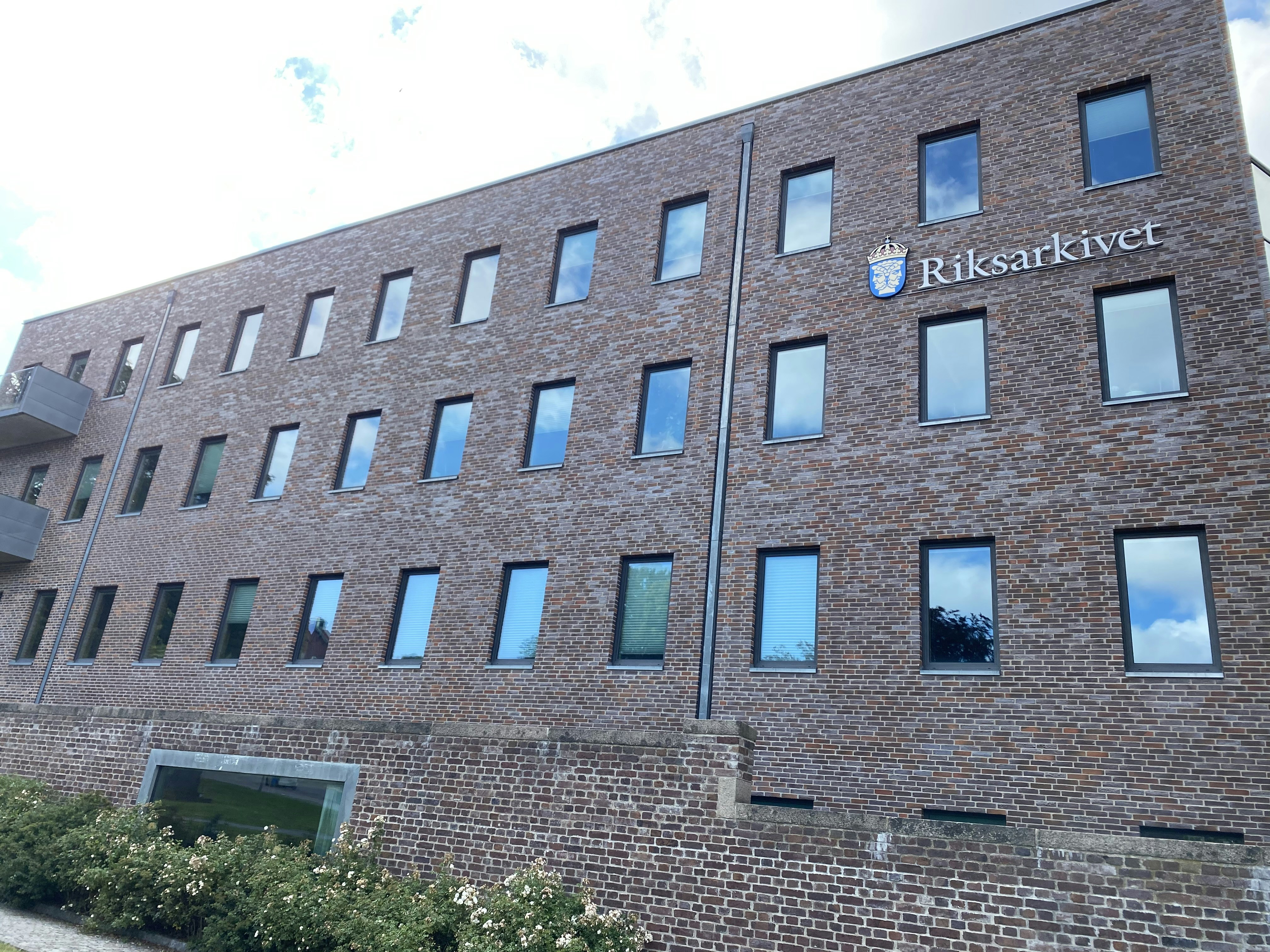 Modern brick building with reflective windows under a partly cloudy sky.