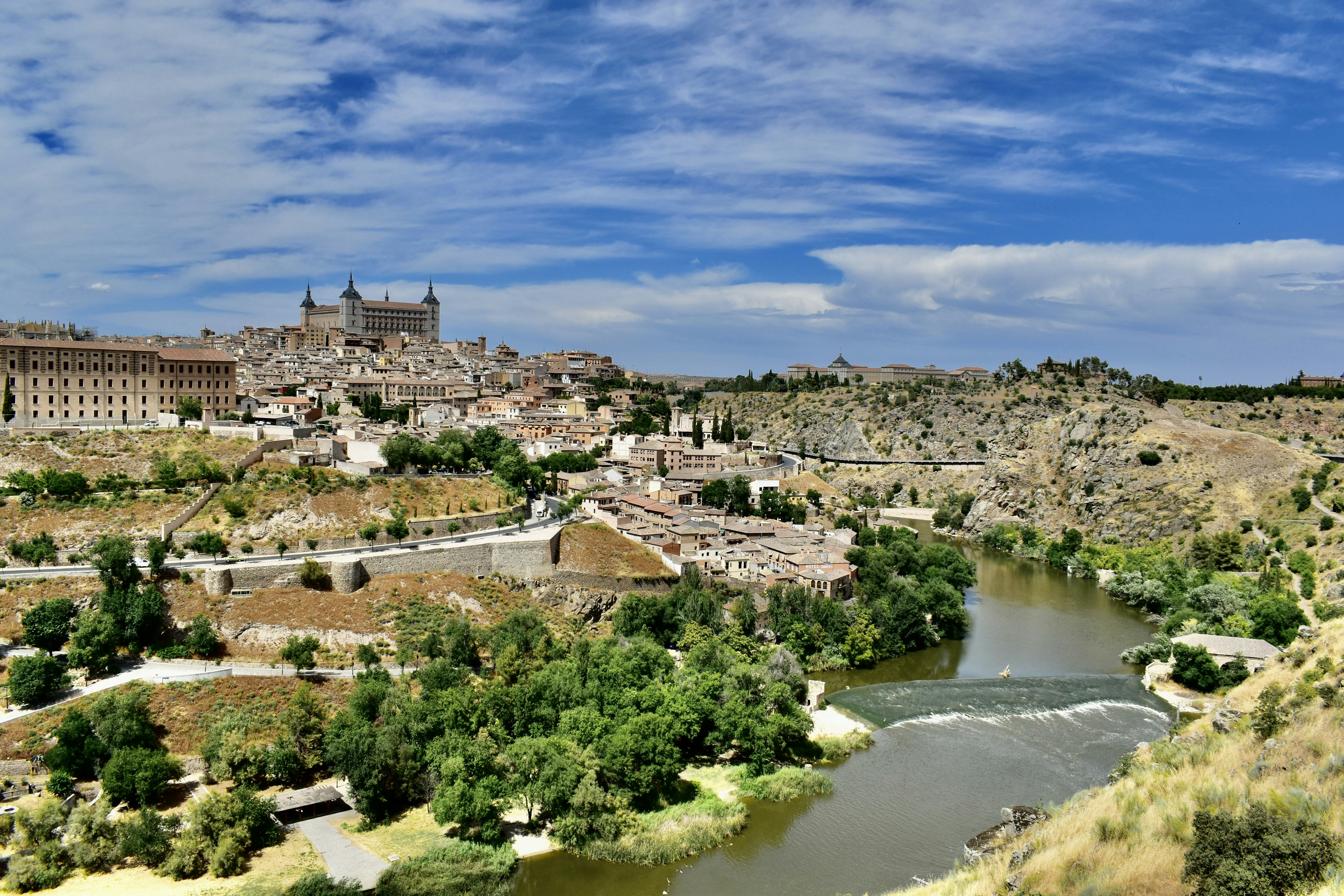 River winding through a historic cityscape with ancient architecture under a bright, expansive sky.