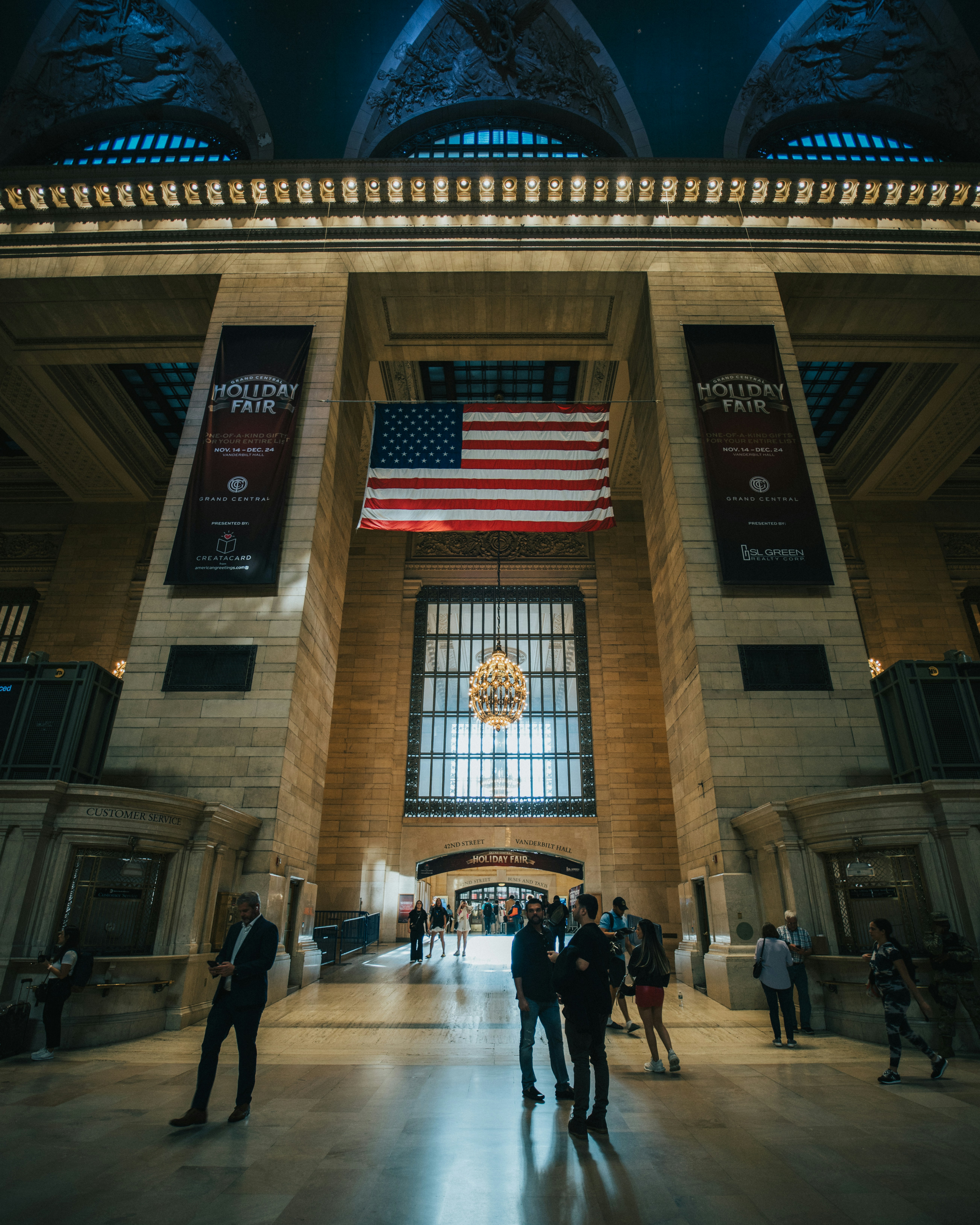 A group of people walking inside a building with a flag on the ceiling ...