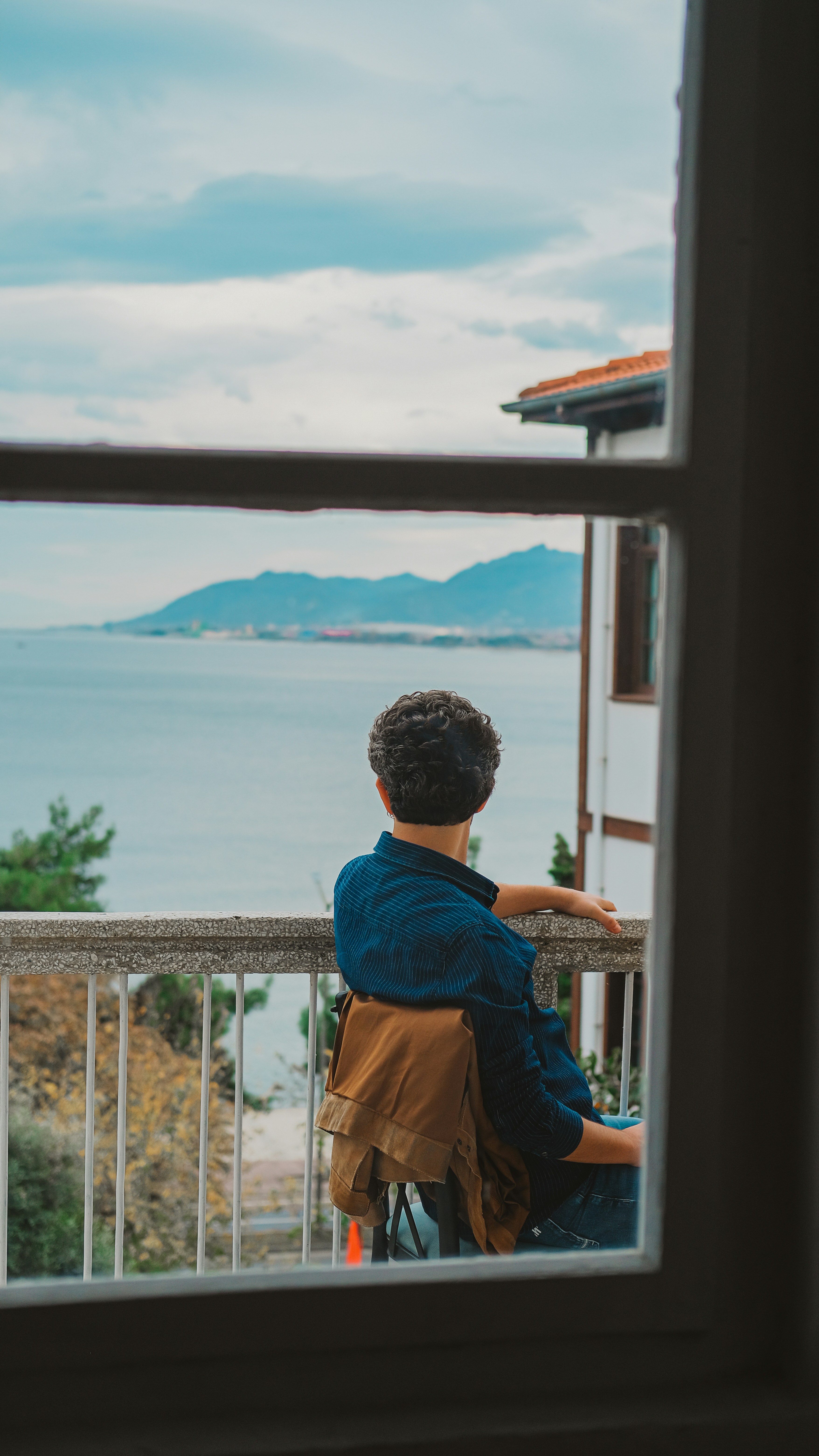 A boy sitting on a balcony looking out at the water photo – Free Child ...