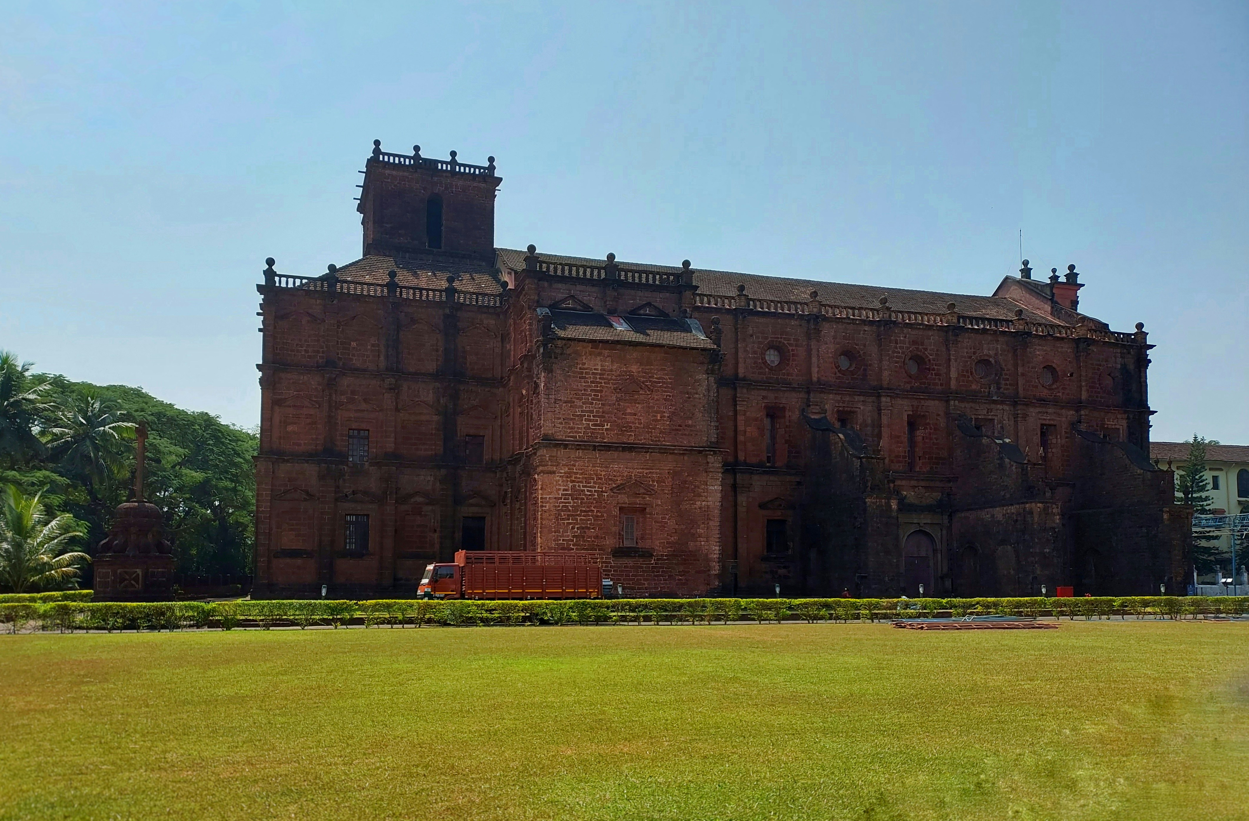Photograph of a red brick fortress bathed in sunlight on a manicured lawn beneath a clear blue sky.