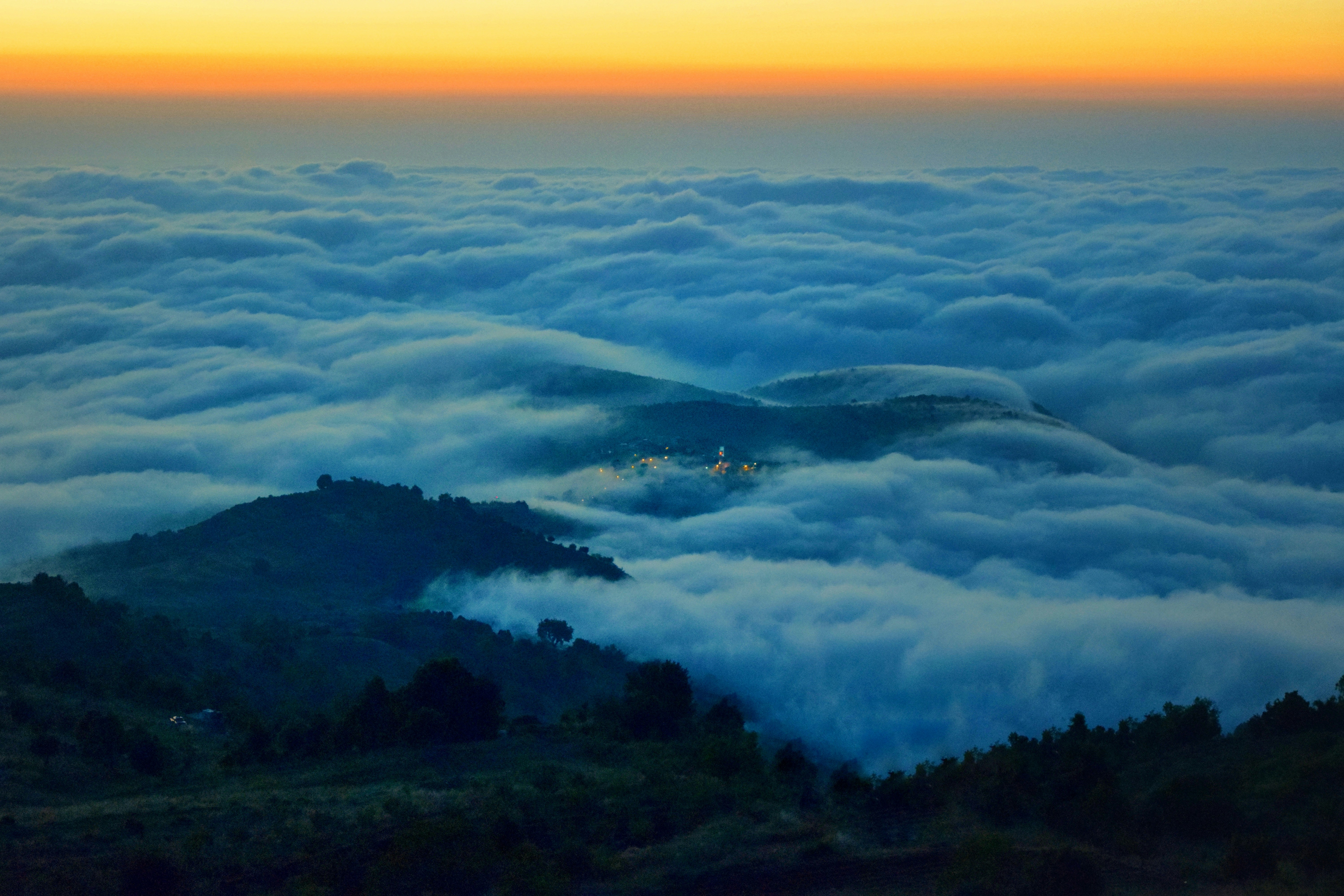 Rolling clouds blanket a mountain landscape under an orange-tinted sunrise.